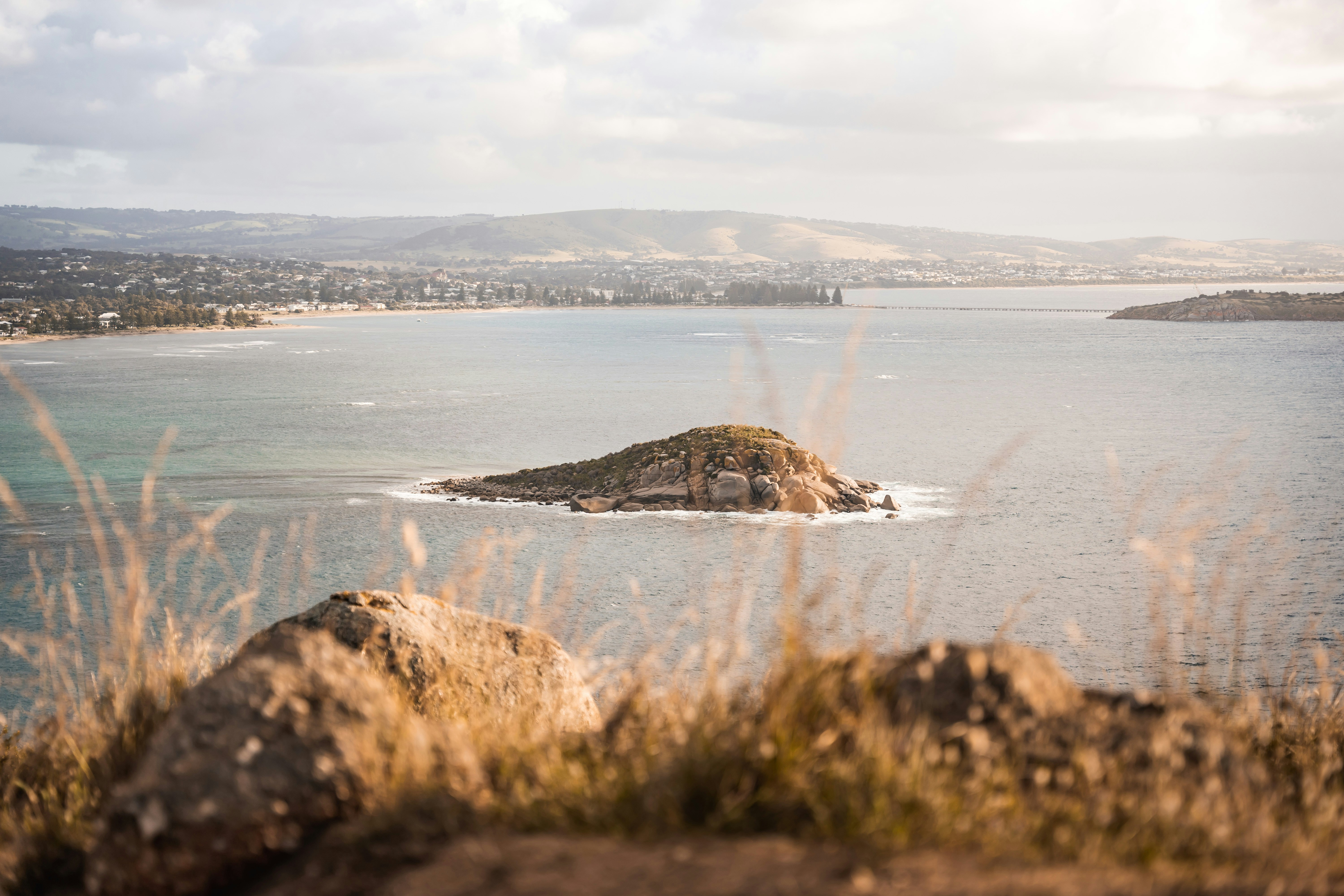 A tranquil view of a small island surrounded by shimmering waters, framed by lush grass in the foreground. The scene captures the essence of nature's calmness.