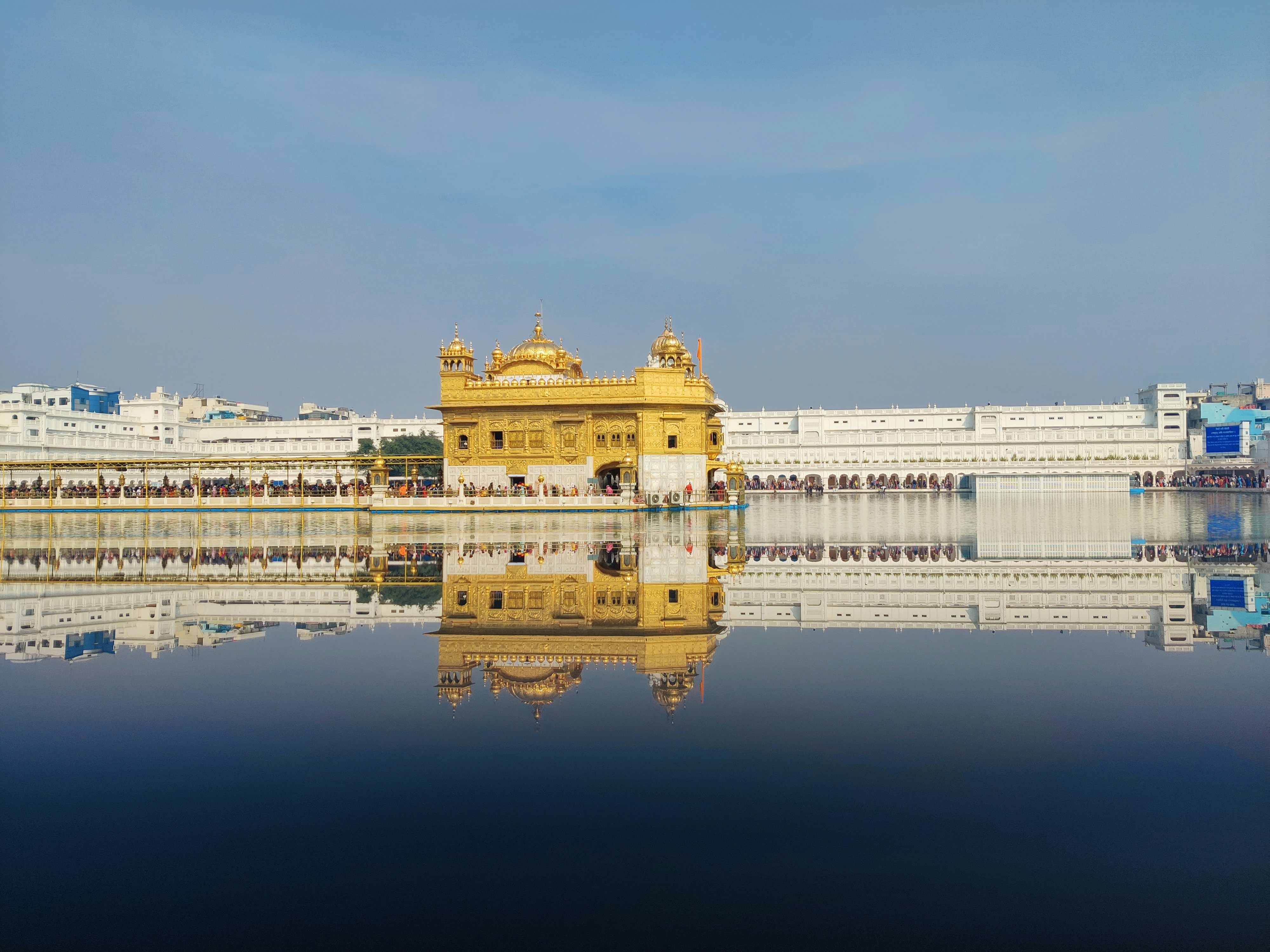 Golden temple reflected in a tranquil blue lake under a clear sky.