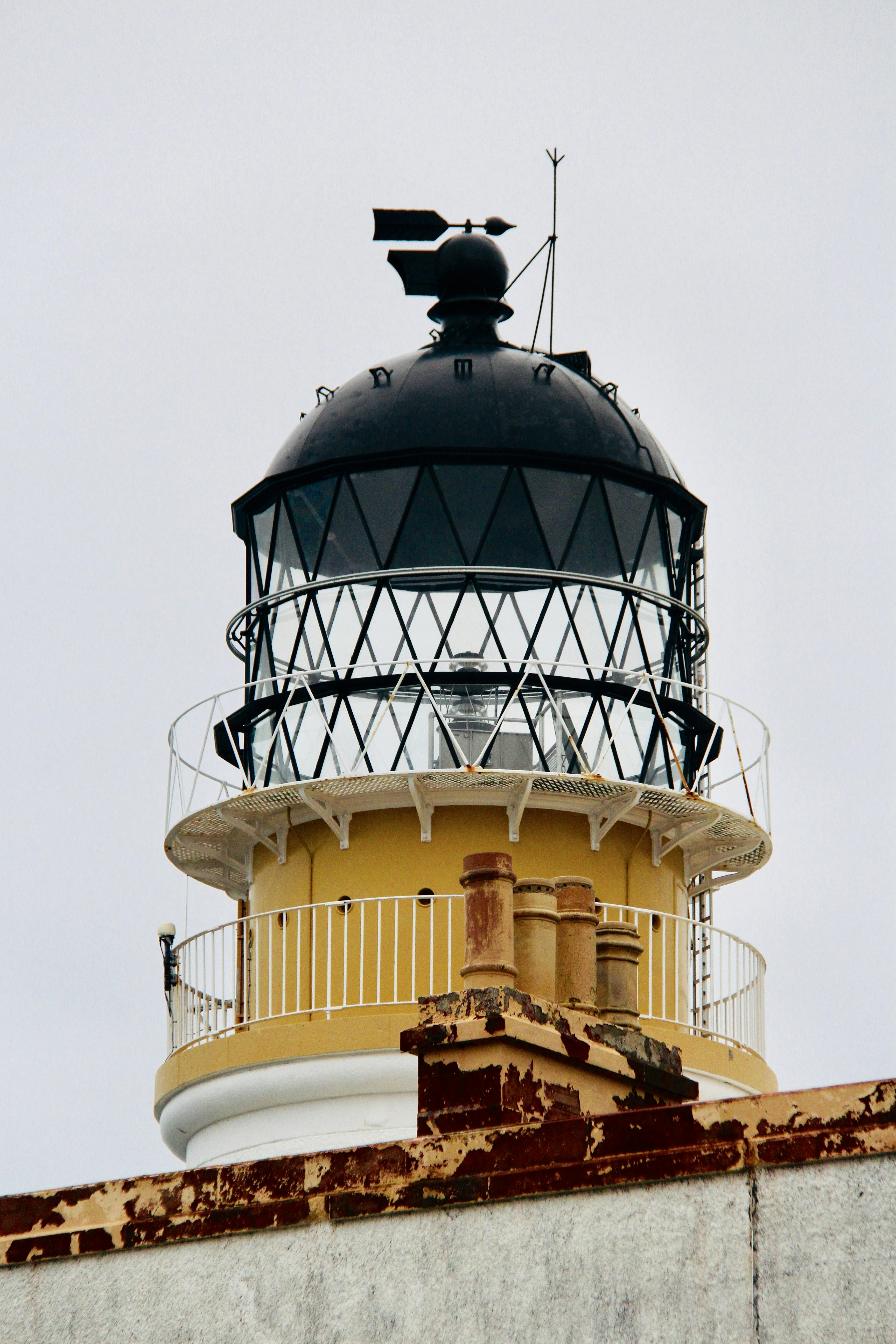 A majestic lighthouse with a black dome and intricate glasswork, perched atop a weathered structure. The scene conveys a sense of maritime history.