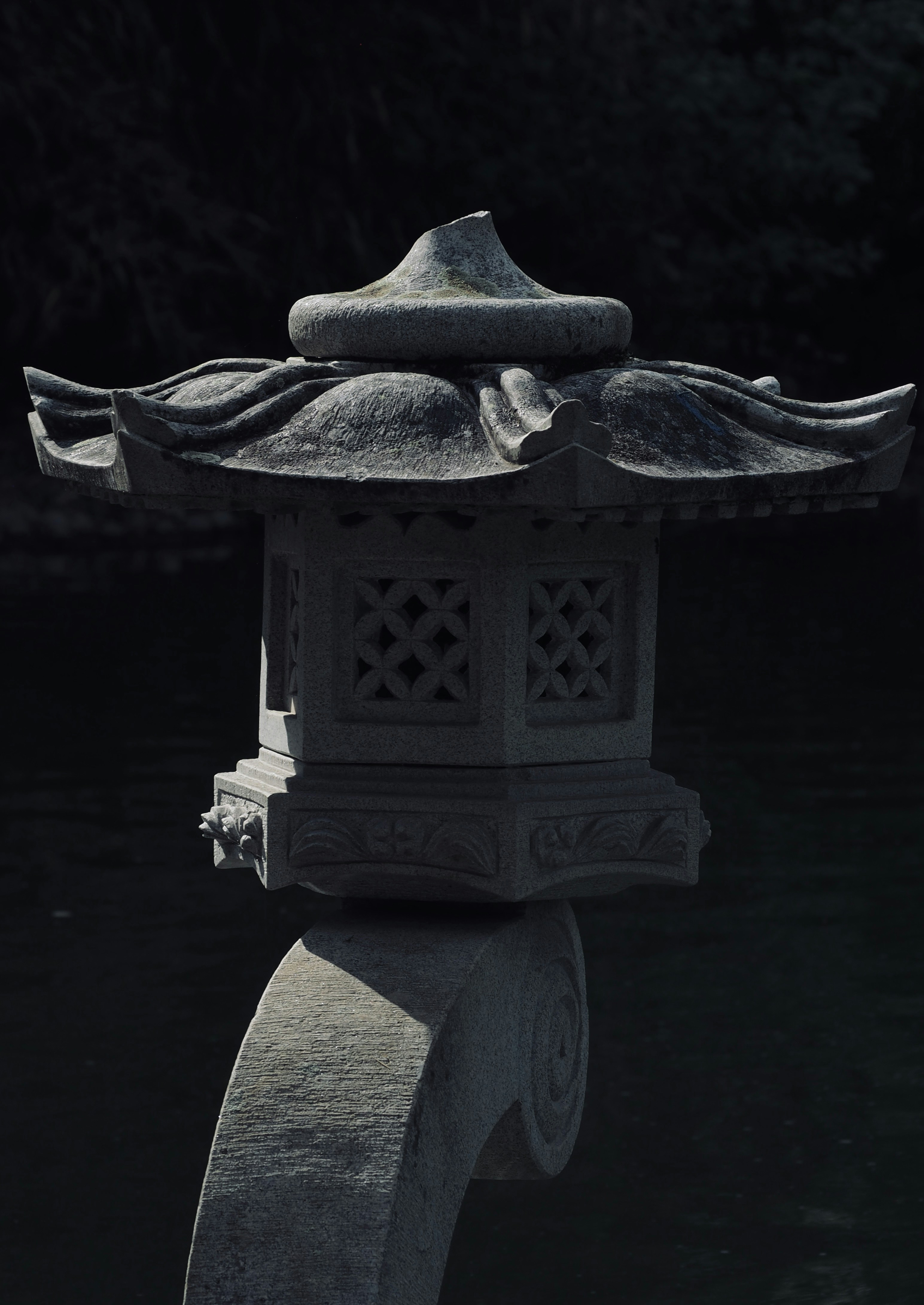 Intricately designed stone lantern perched on a curved pedestal, reflecting the serene ambiance of its surroundings.
