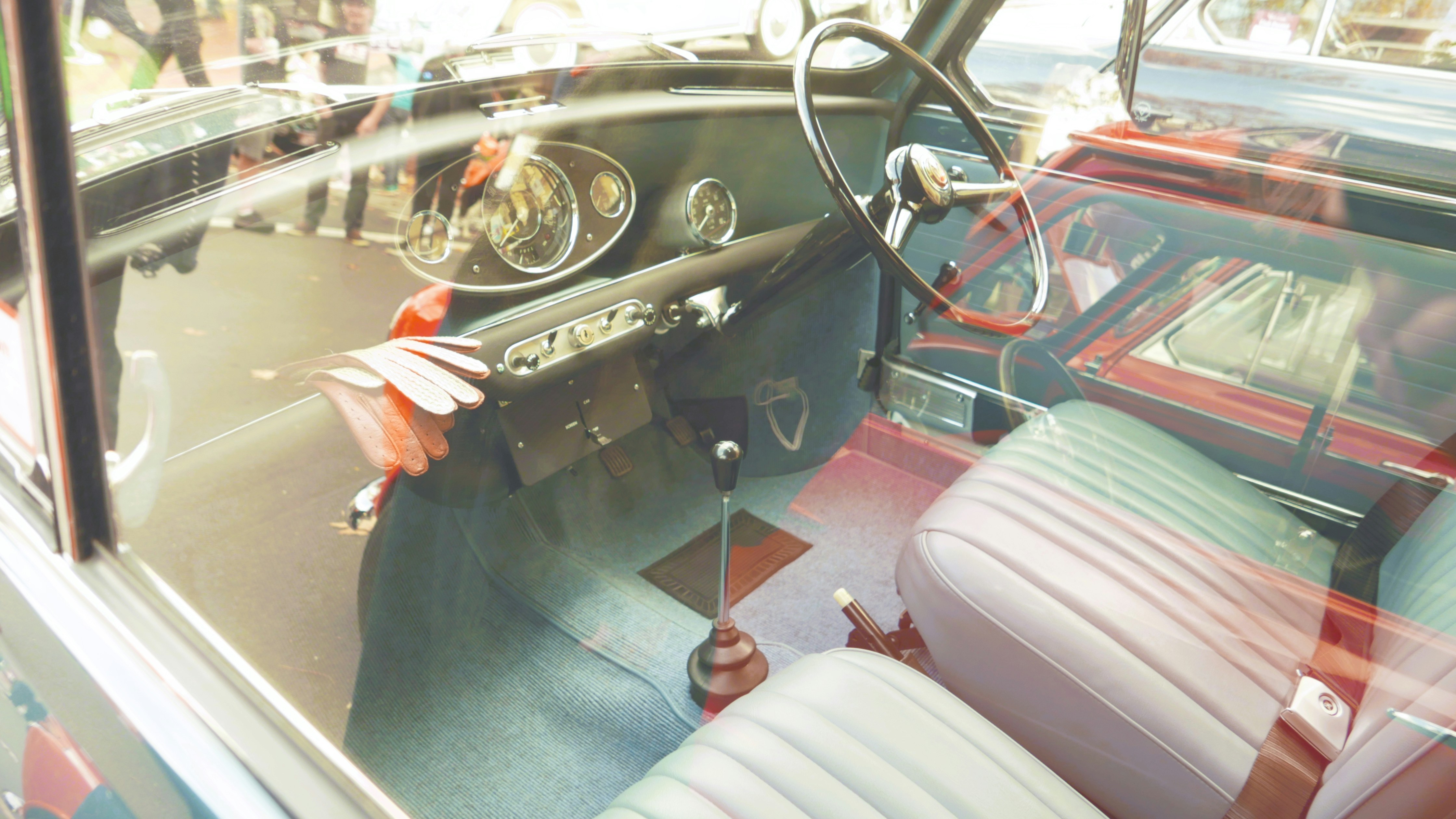Classic car interior with vintage leather gloves on the dashboard, reflecting the vibrant street scene outside.
