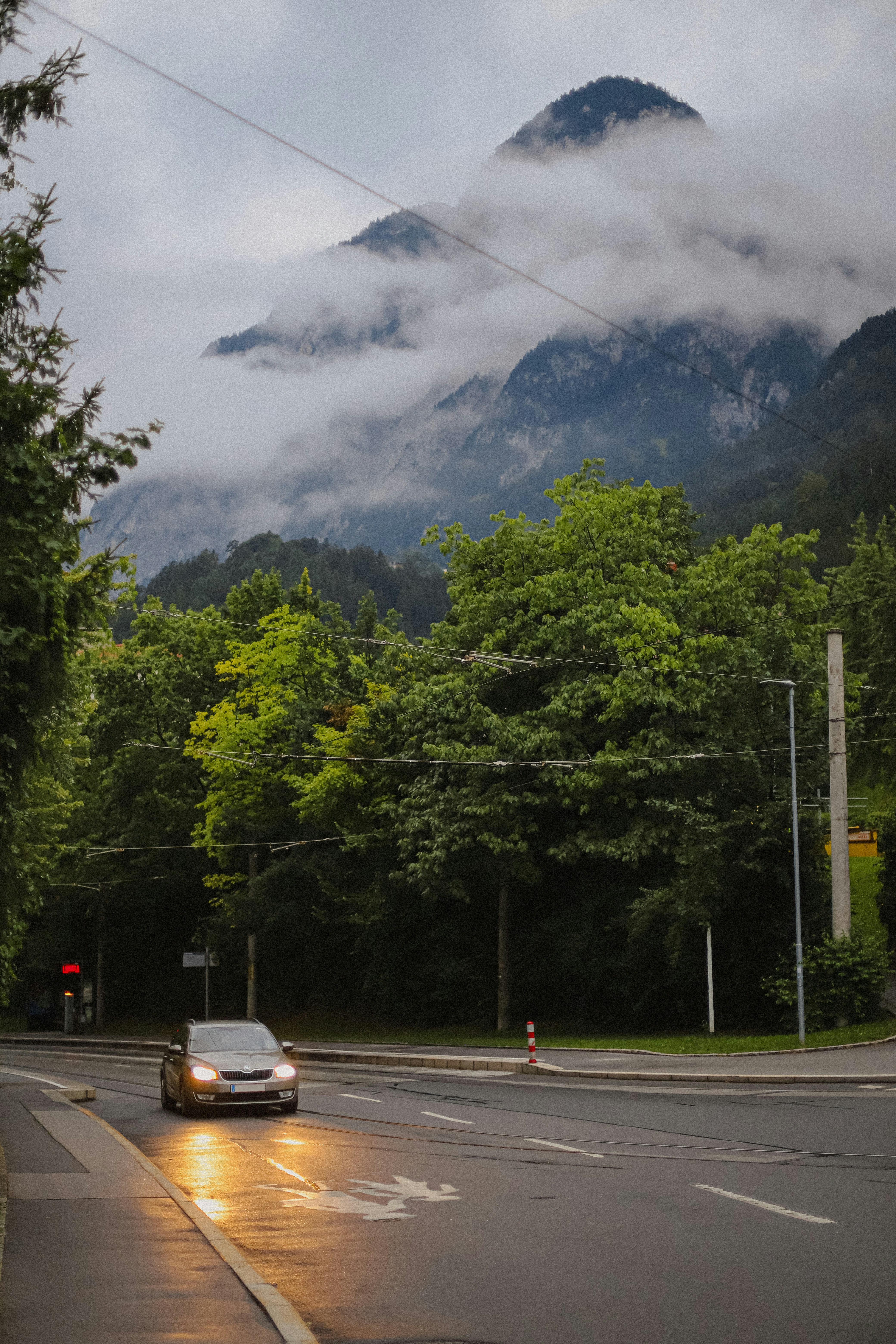 A sleek car navigates a winding road surrounded by lush greenery and misty mountains, capturing a moment of serene travel.