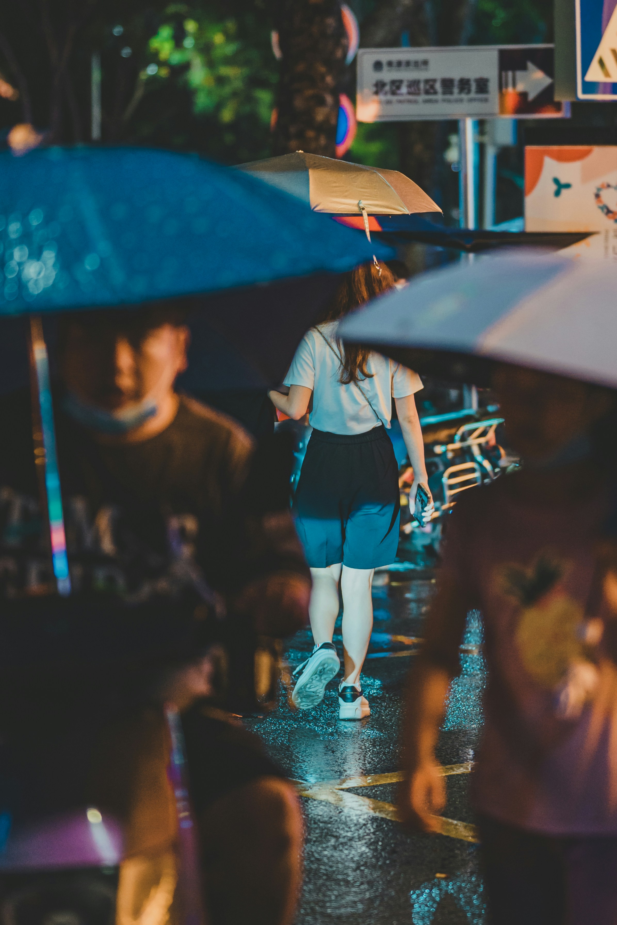 Rain-Soaked Crosswalk: A Lone Pedestrian Amid Neon Umbrellas