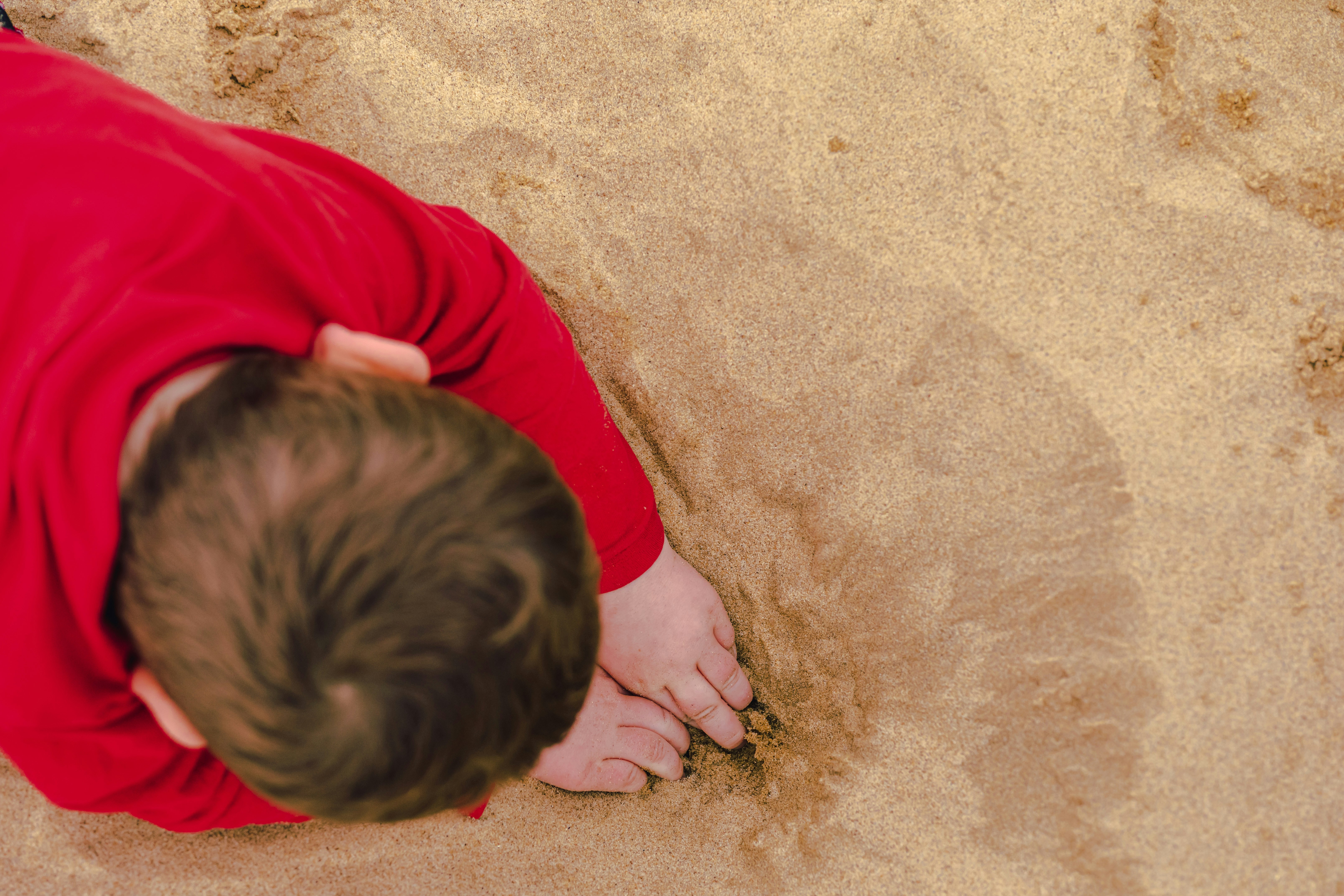Red-clad child digging into warm sand under soft light