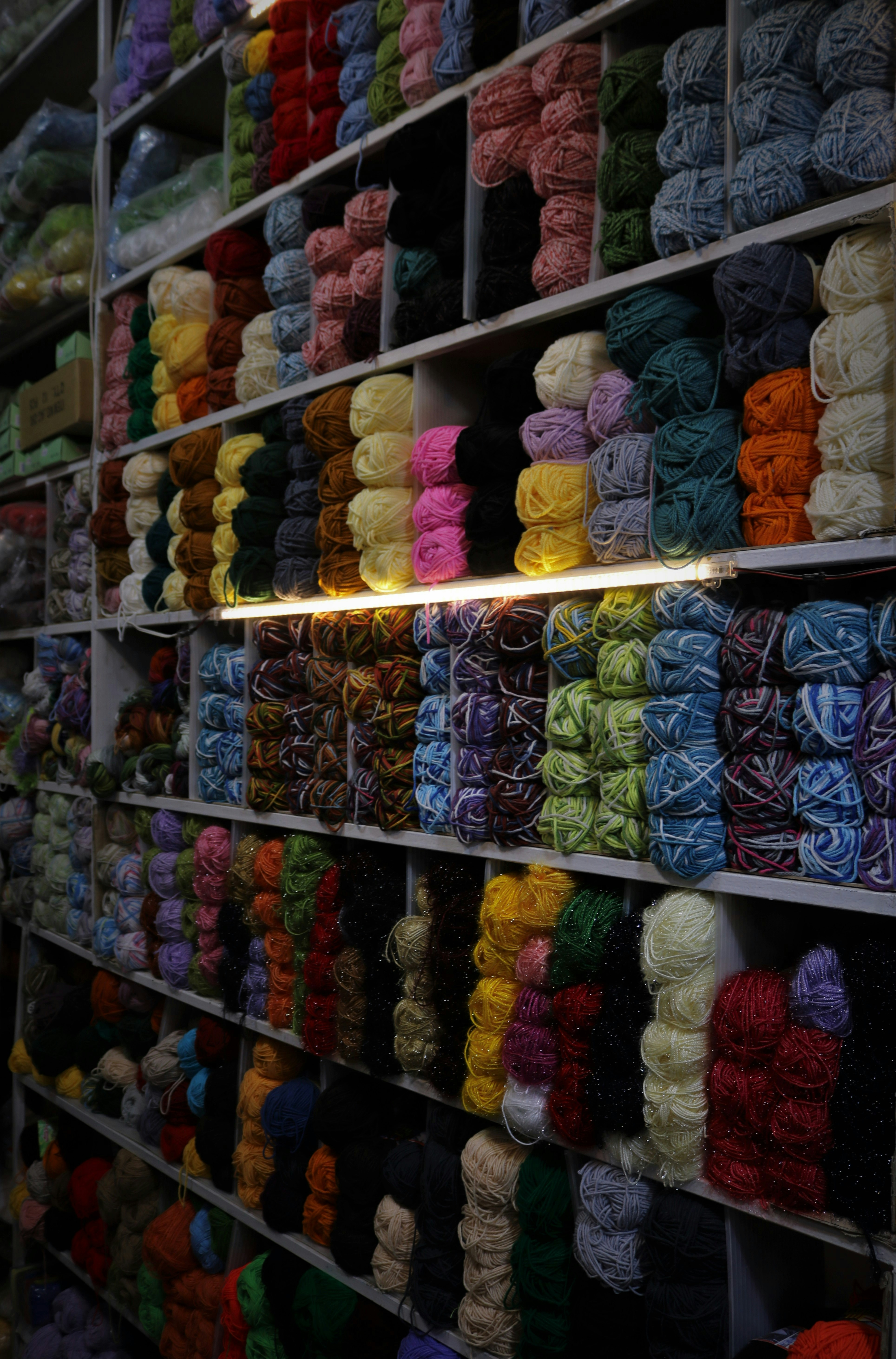 Colorful spools of yarn neatly arranged on shelves, showcasing a vibrant spectrum of hues and textures. The display highlights the artistry of textile crafting.