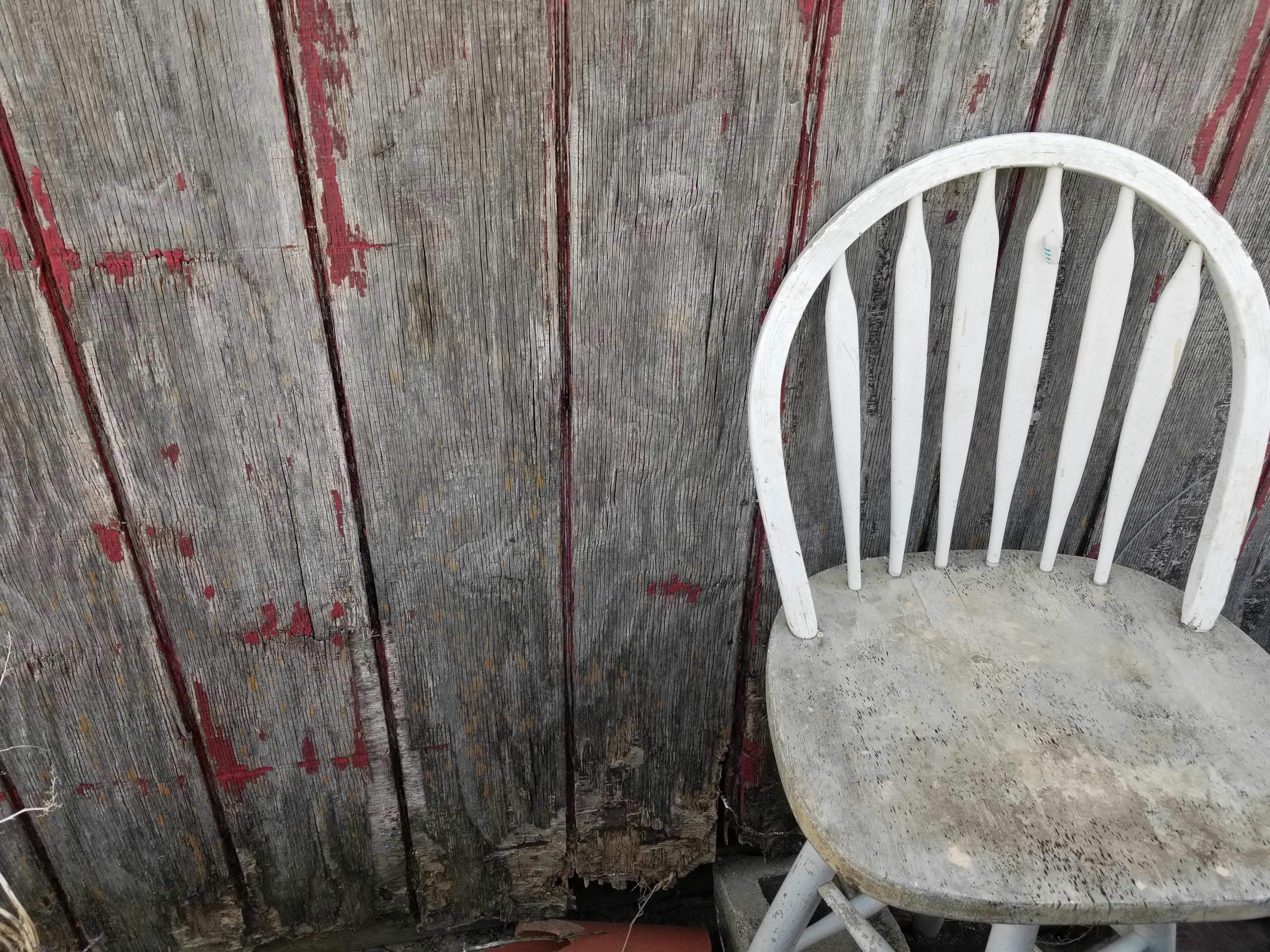 A weathered white chair positioned beside a peeling red and gray wooden wall, showcasing the passage of time through its textures.