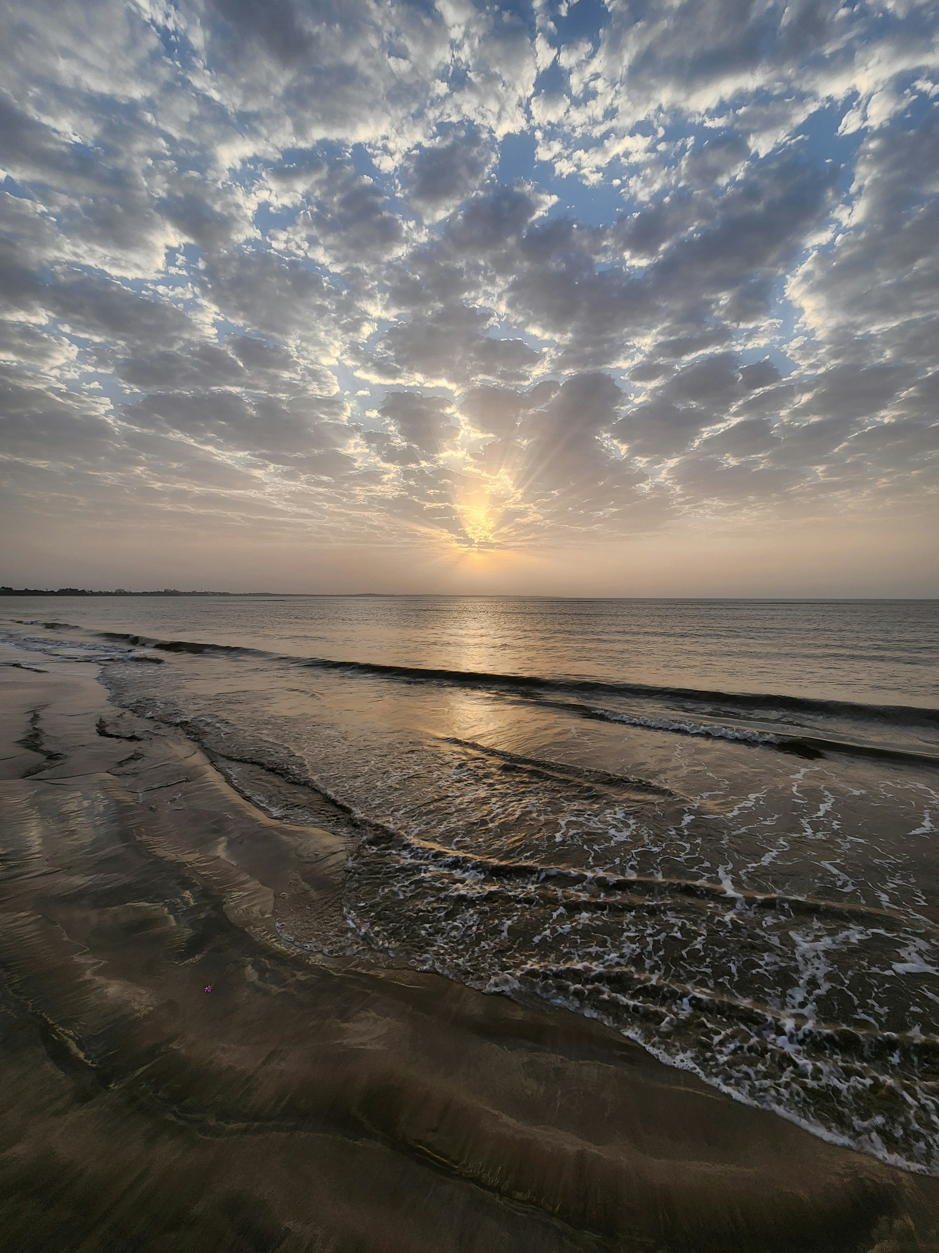 Dusk's Quiet Symphony: Sun Breaks Through Cloud-Spread over a Shimmering Shore