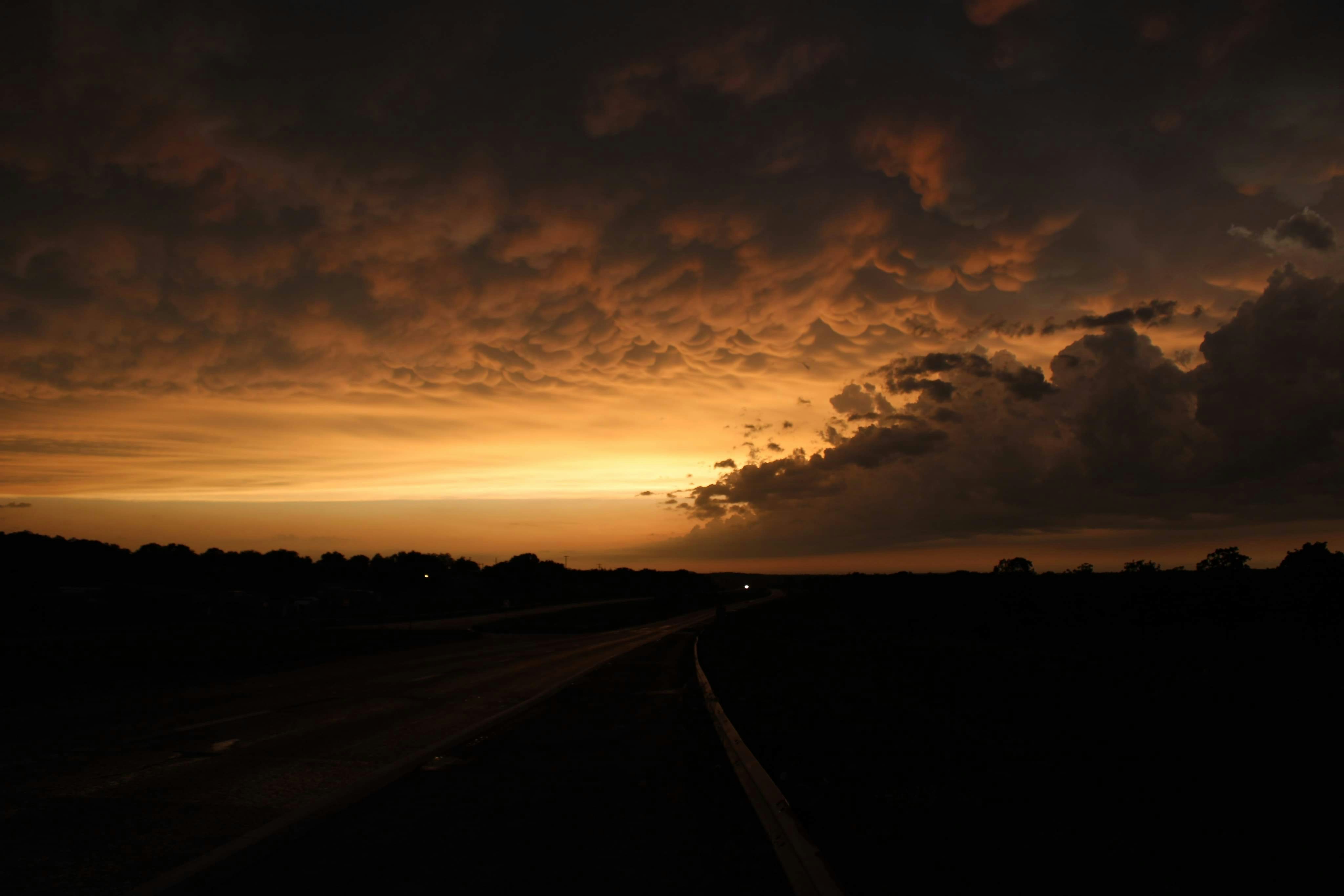 the sun is setting over a highway with dark clouds