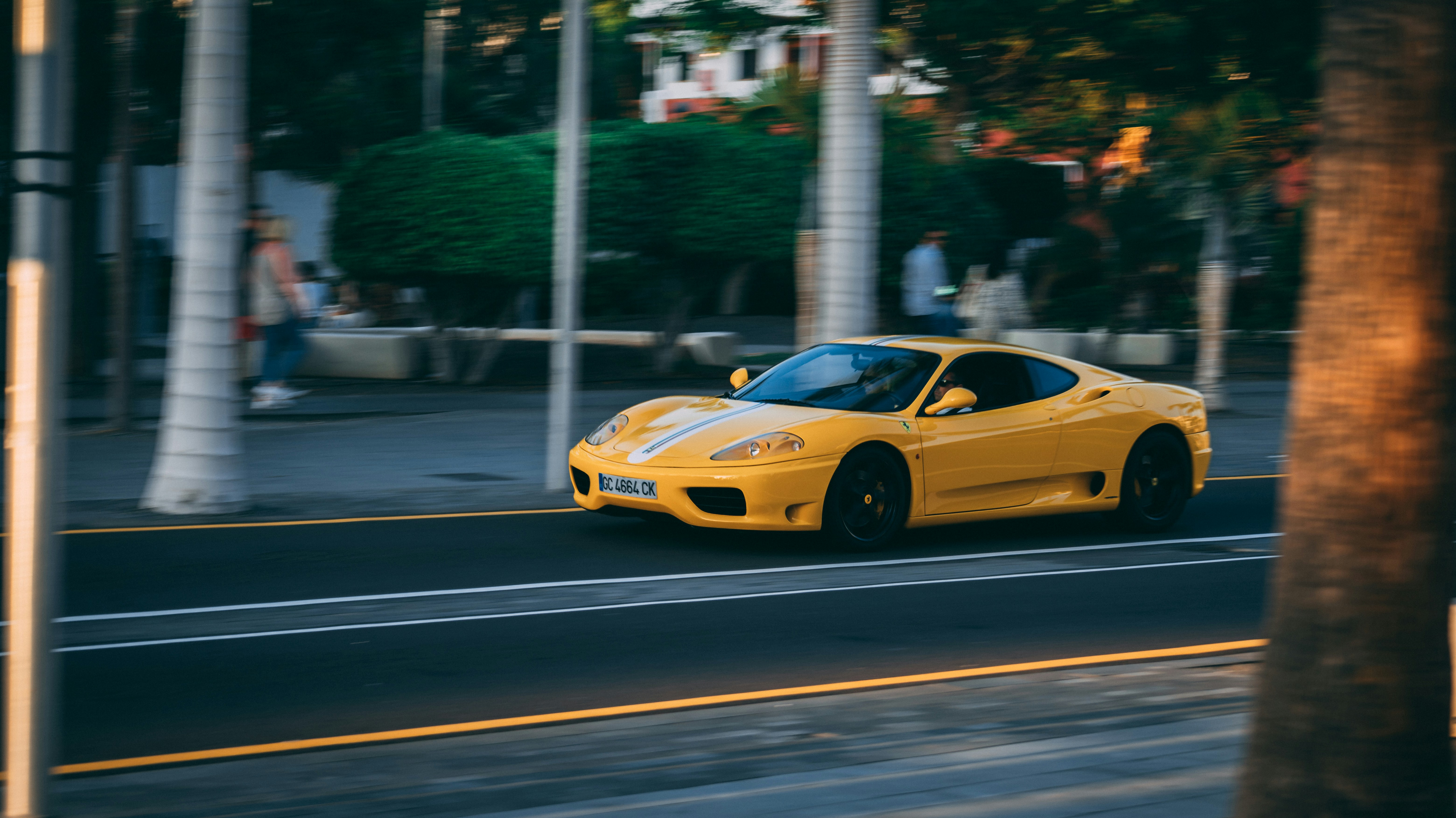 Sunlit Velocità: Yellow Ferrari on a Palm-Lined City Boulevard
