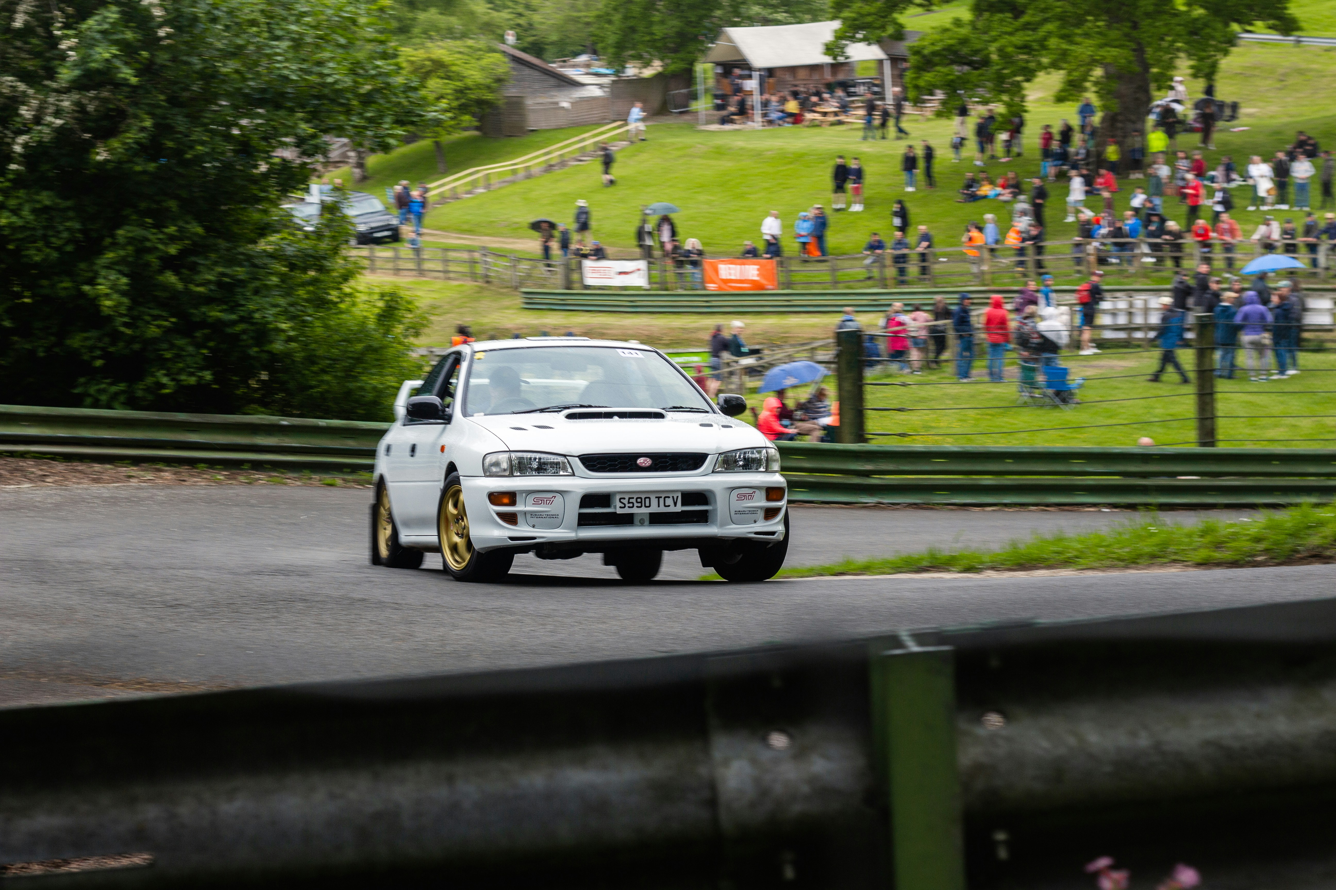 a white car driving down a road next to a crowd of people