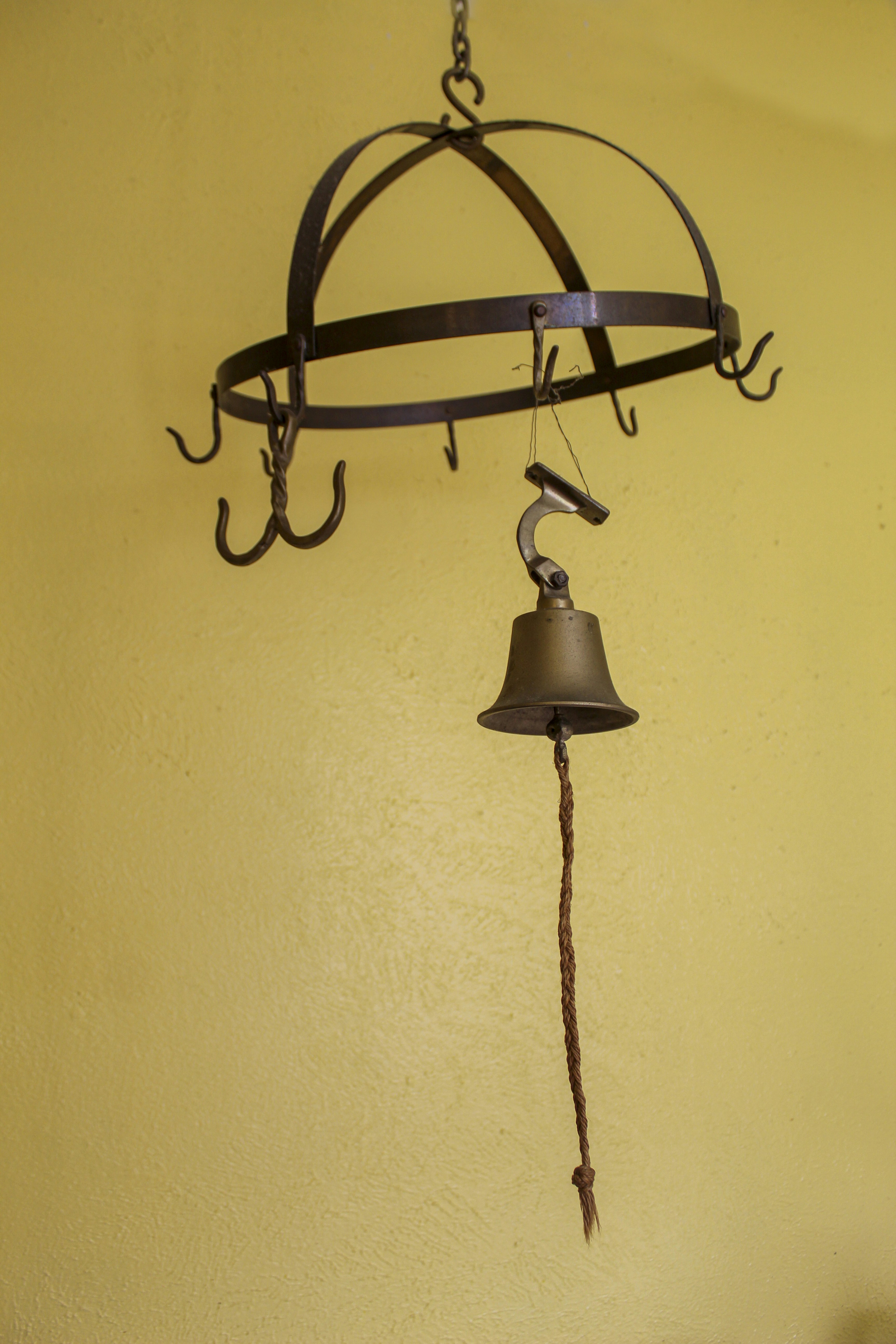 Bell, Rope, and Ring: Rusted Details on a Sunlit Yellow Wall