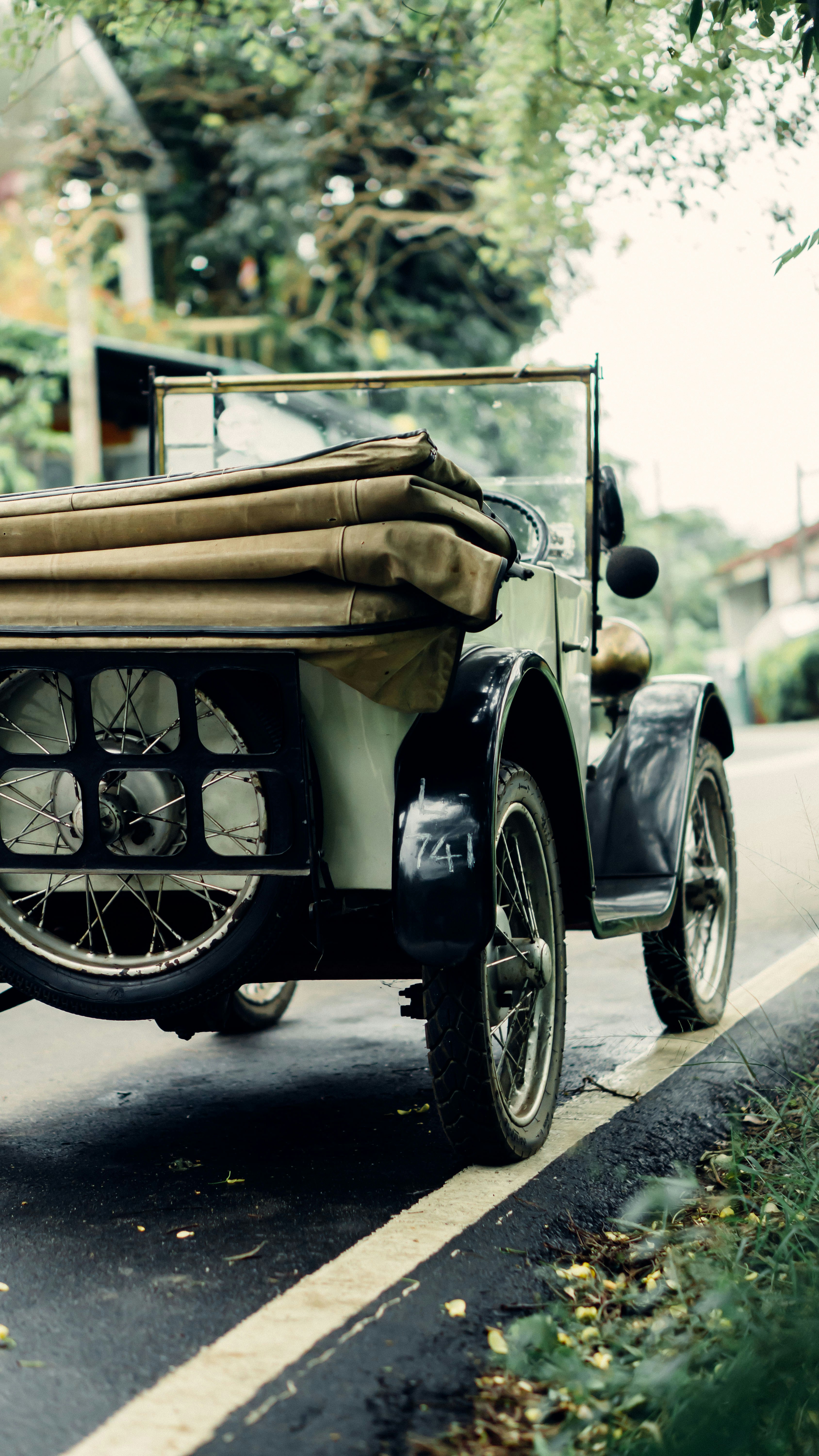 Classic convertible parked along a serene road, showcasing its retro design and details. The scene is framed by lush greenery.