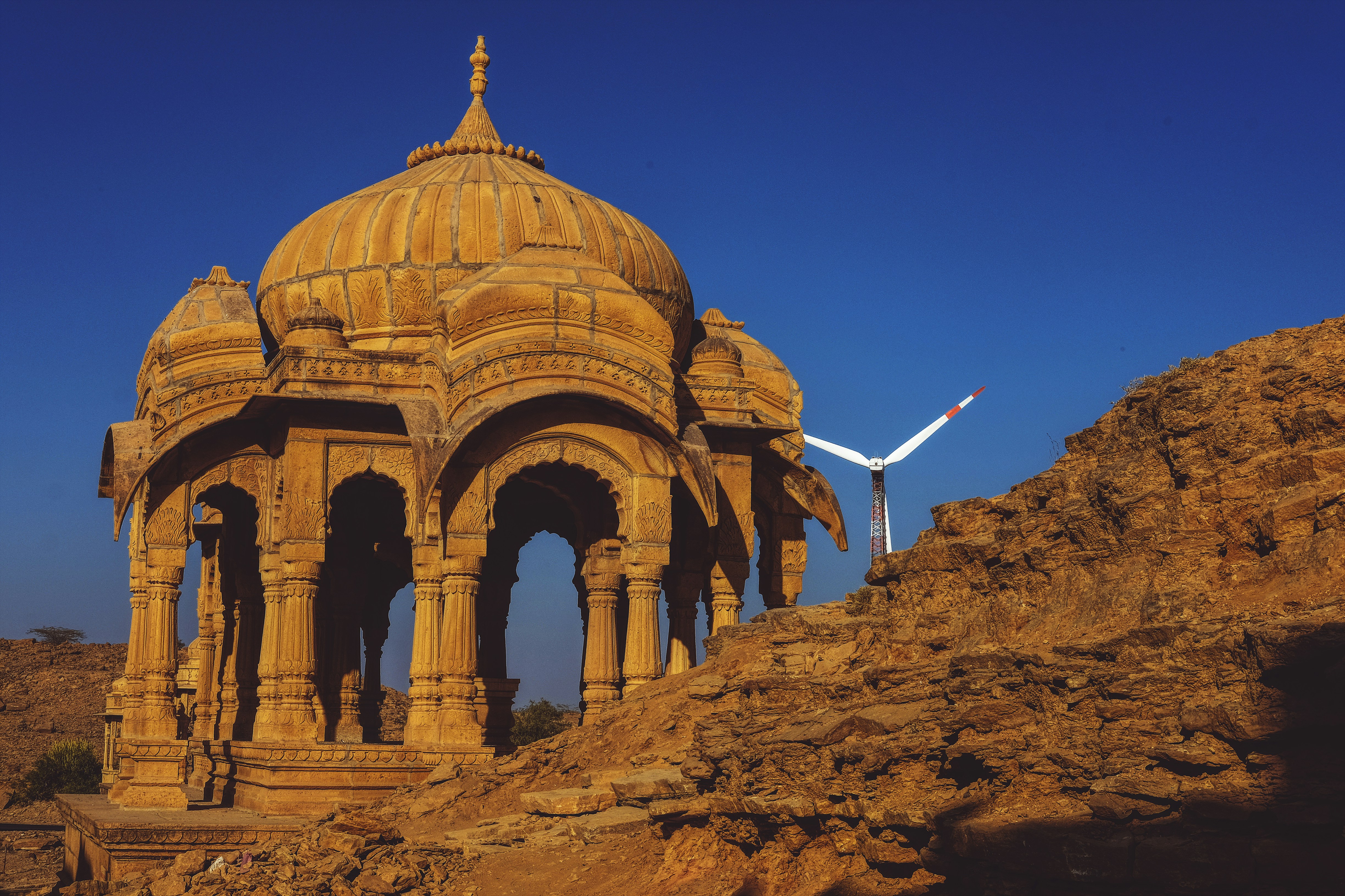 Stone Pavilion in Parched Light: An Ancient Archway with a Modern Wind Turbine in the Background