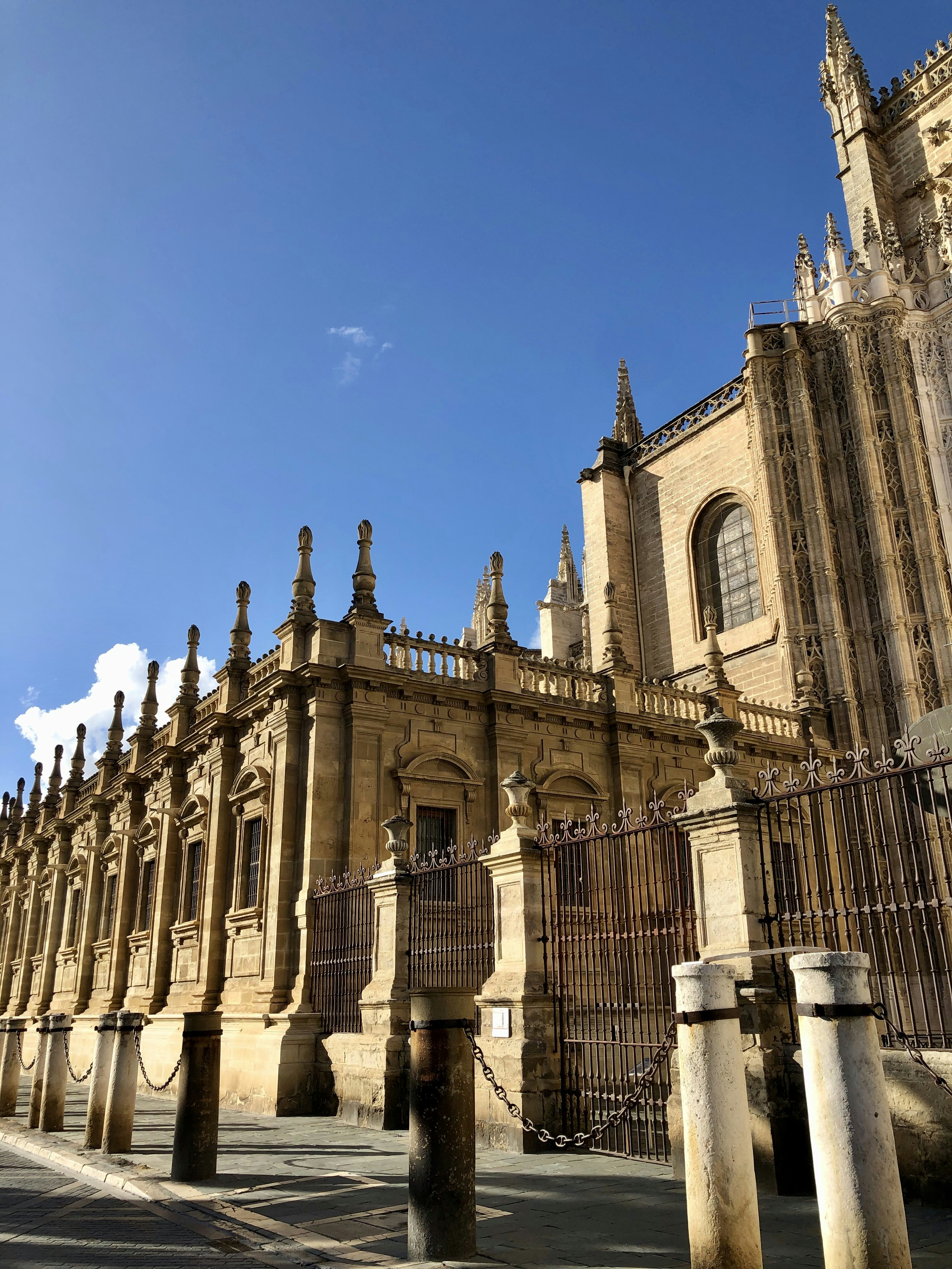 Historic building with intricate stonework and ornate spires, framed by a bright blue sky and scattered clouds.