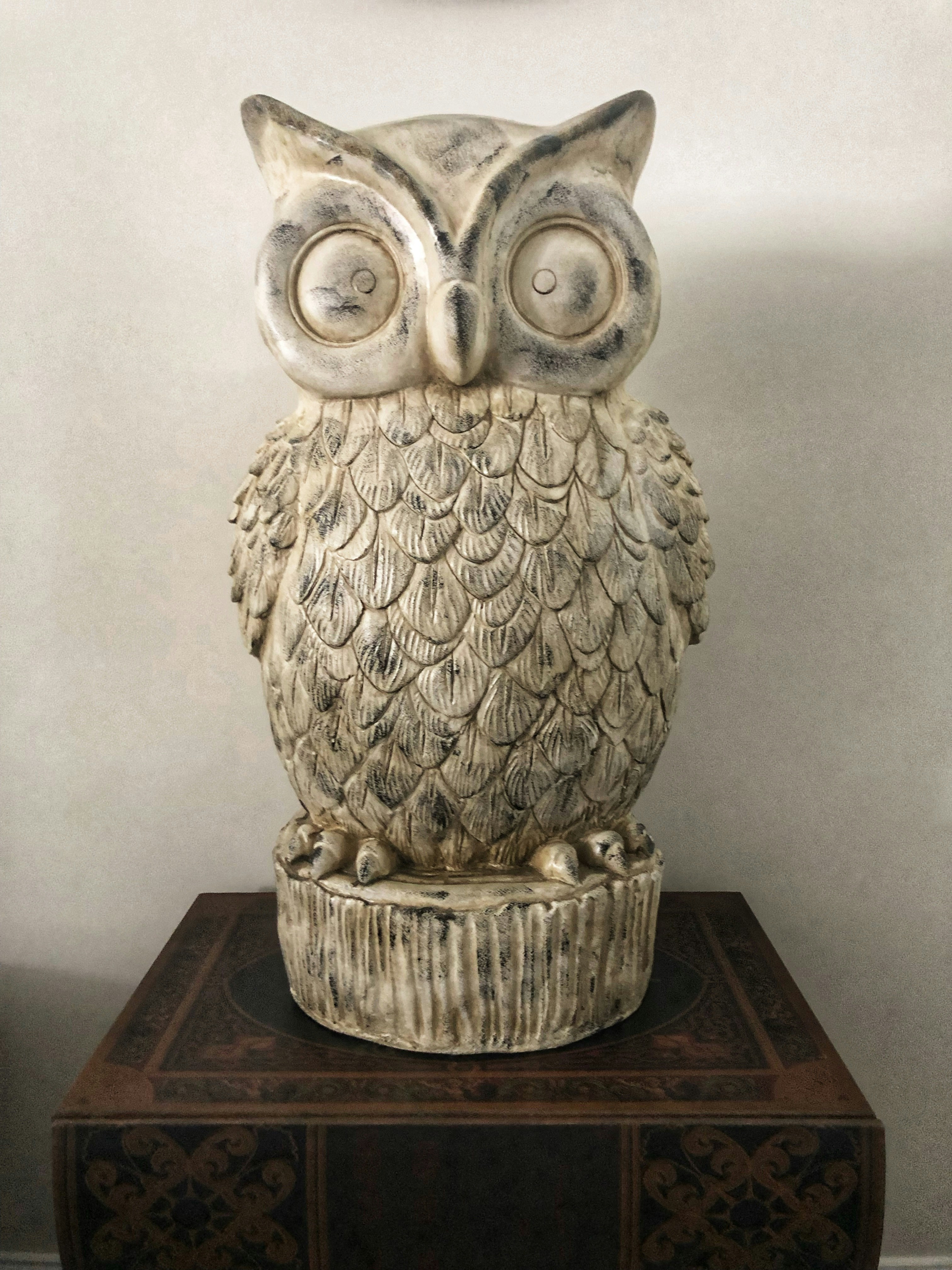A detailed ceramic owl sculpture standing on a wooden table, showcasing intricate feather textures and a whimsical expression.