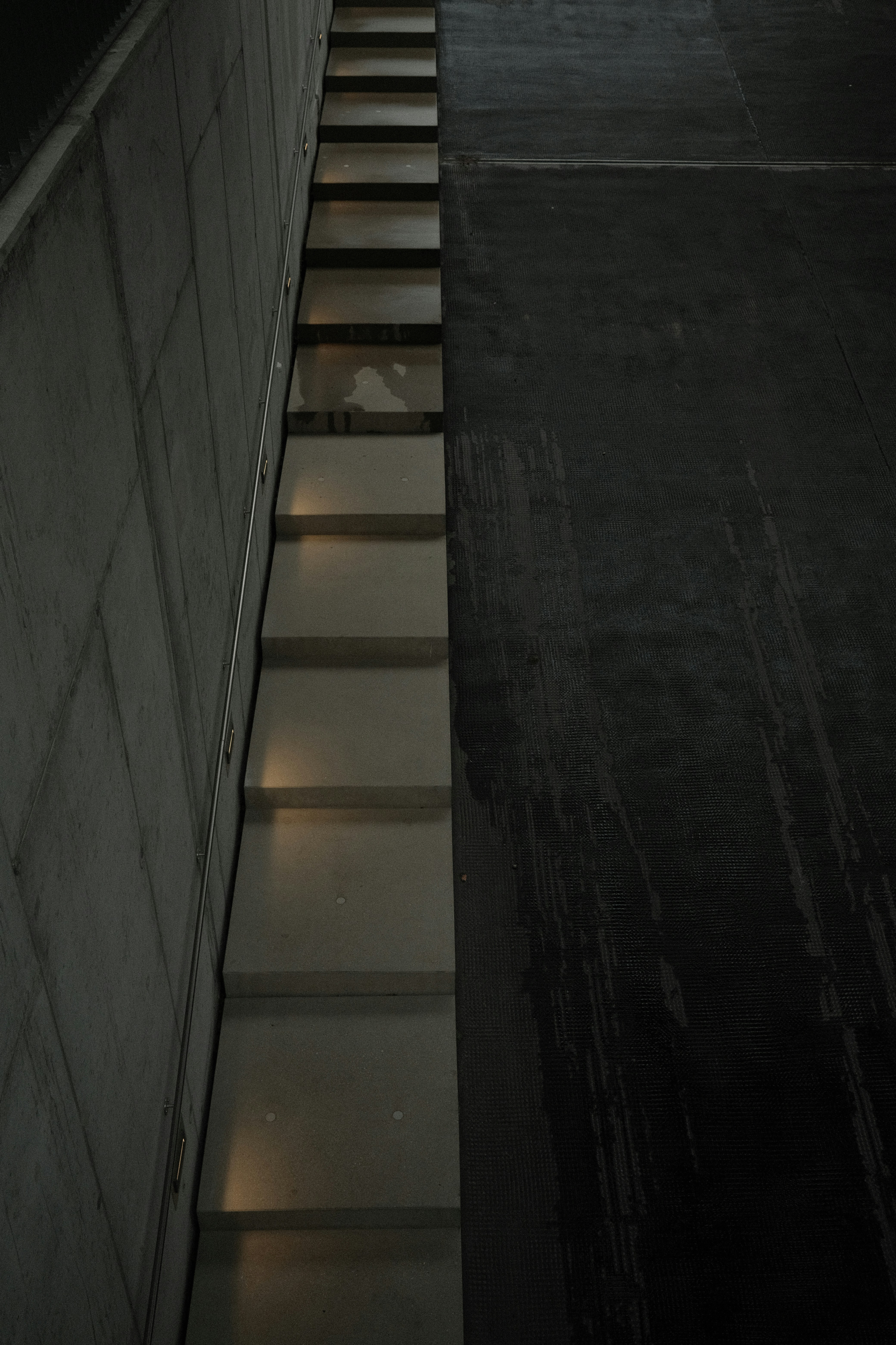 A series of illuminated concrete steps leading up against a textured dark floor, showcasing modern architectural design elements.