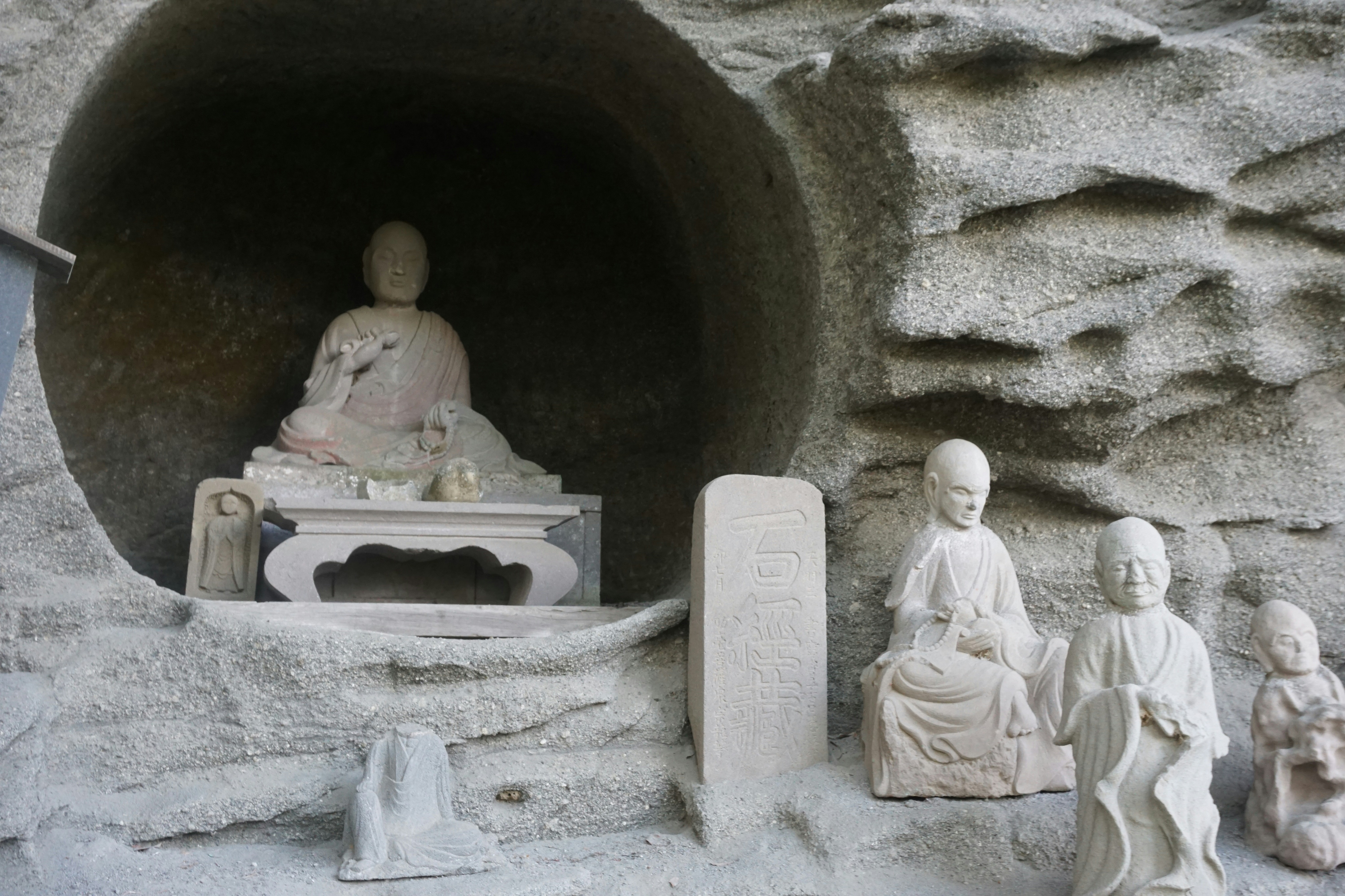 A serene cave housing a seated Buddha statue surrounded by intricately carved stone figures, evoking a sense of peace and spirituality.