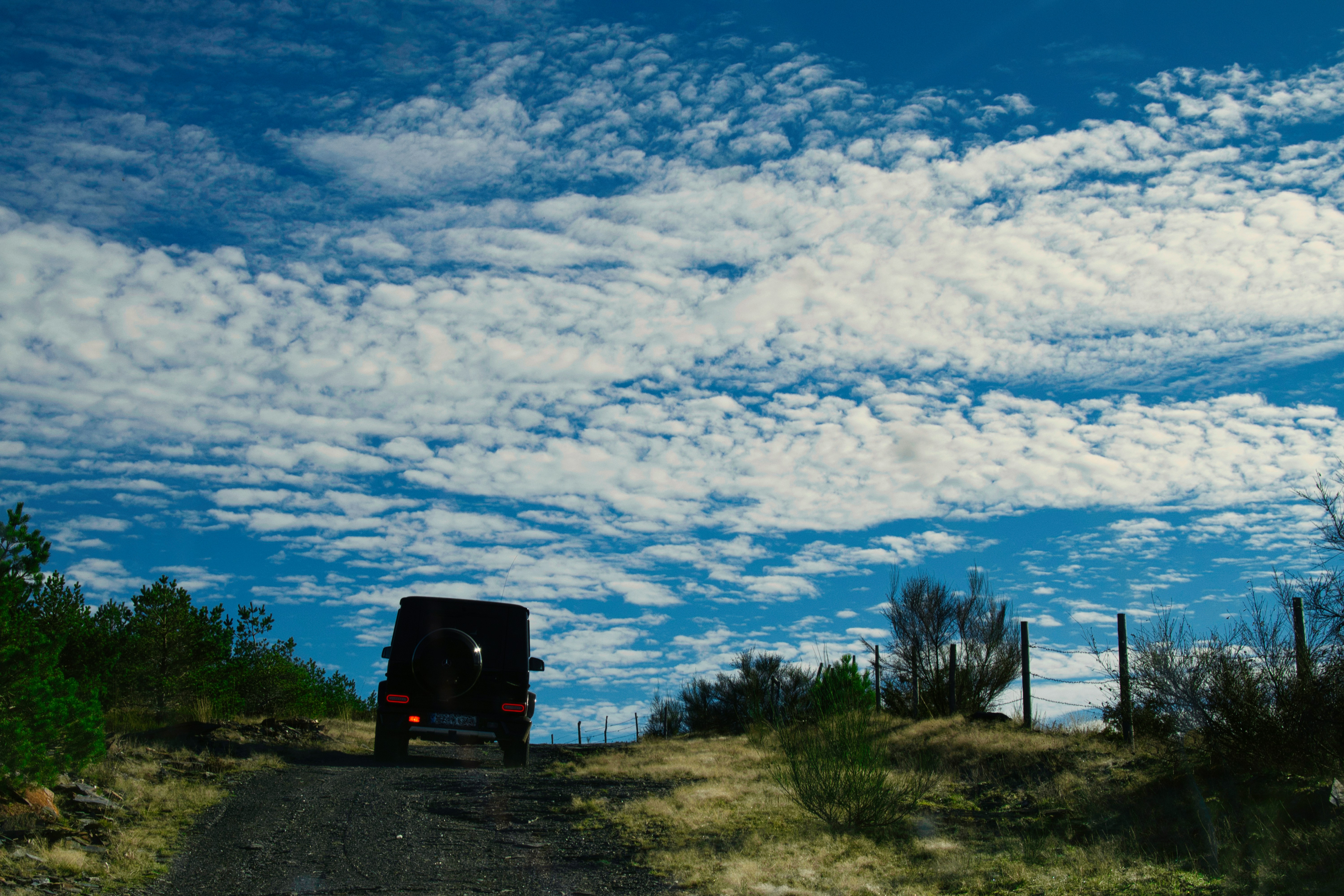 Dusty Road to the Cloudscape: A Black SUV Anchors the Horizon