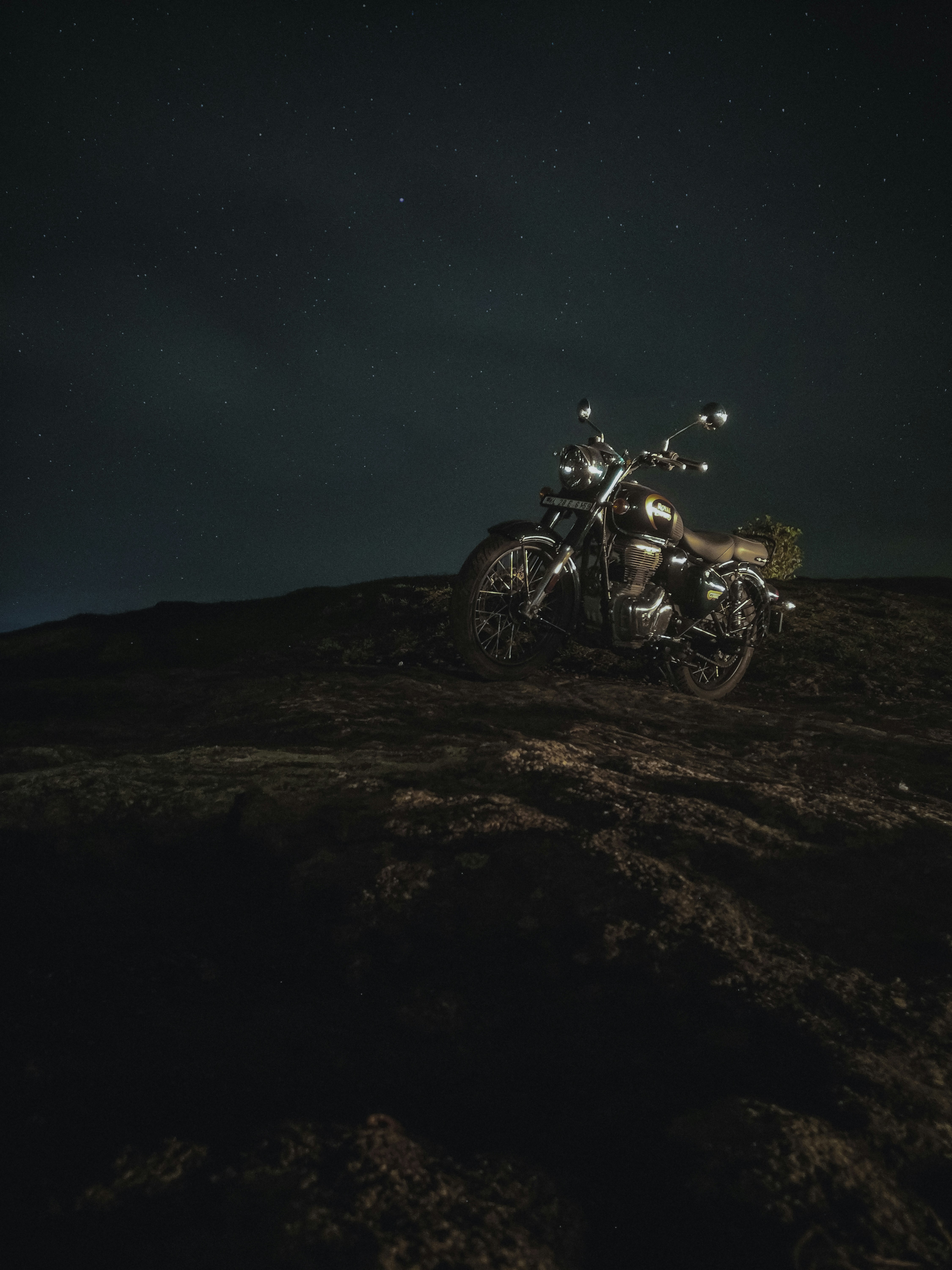 Moonlit Standstill: A vintage motorcycle on a rugged ridge beneath a velvet night sky