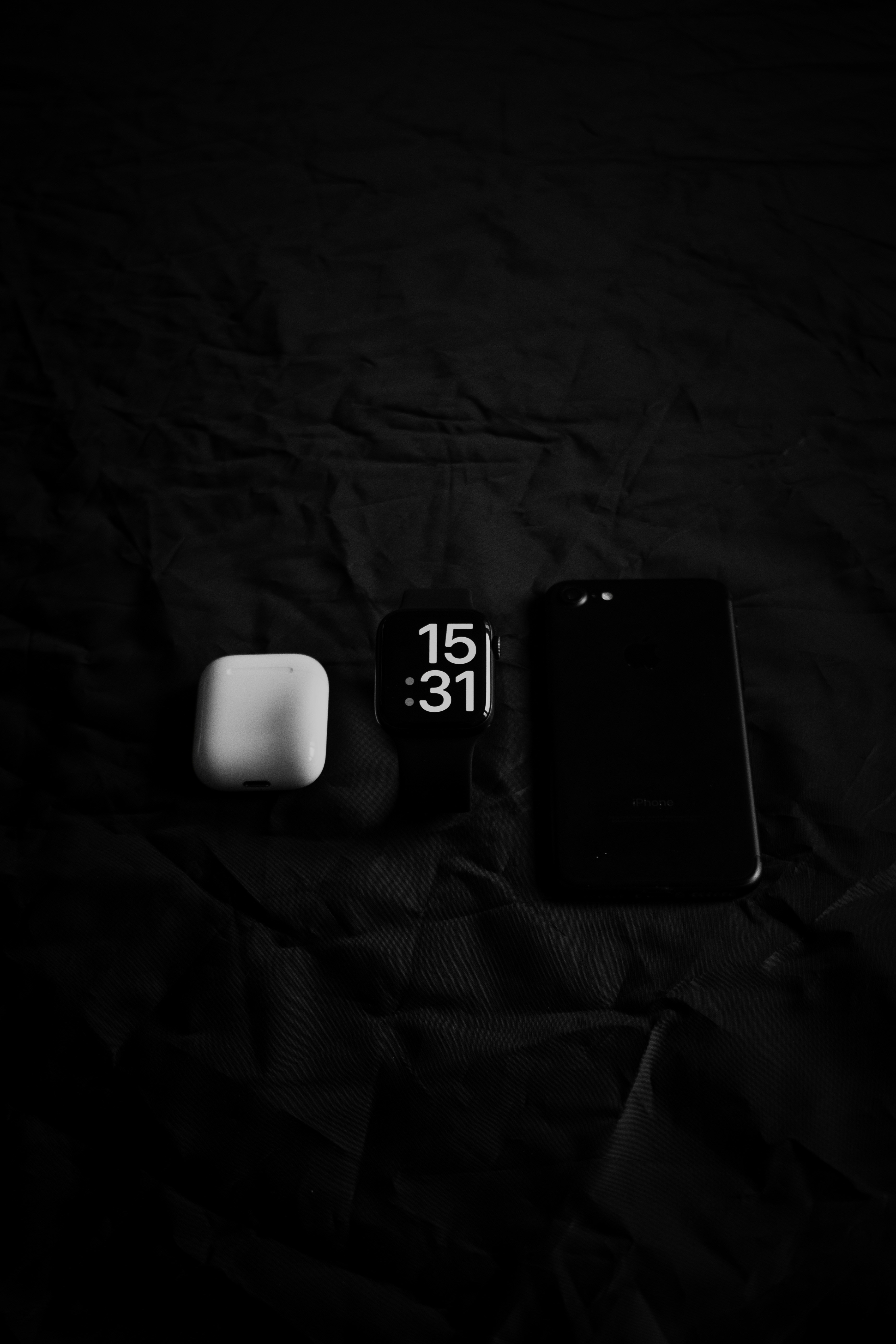 White AirPods, a digital watch displaying the time, and a black smartphone arranged on a textured black surface.