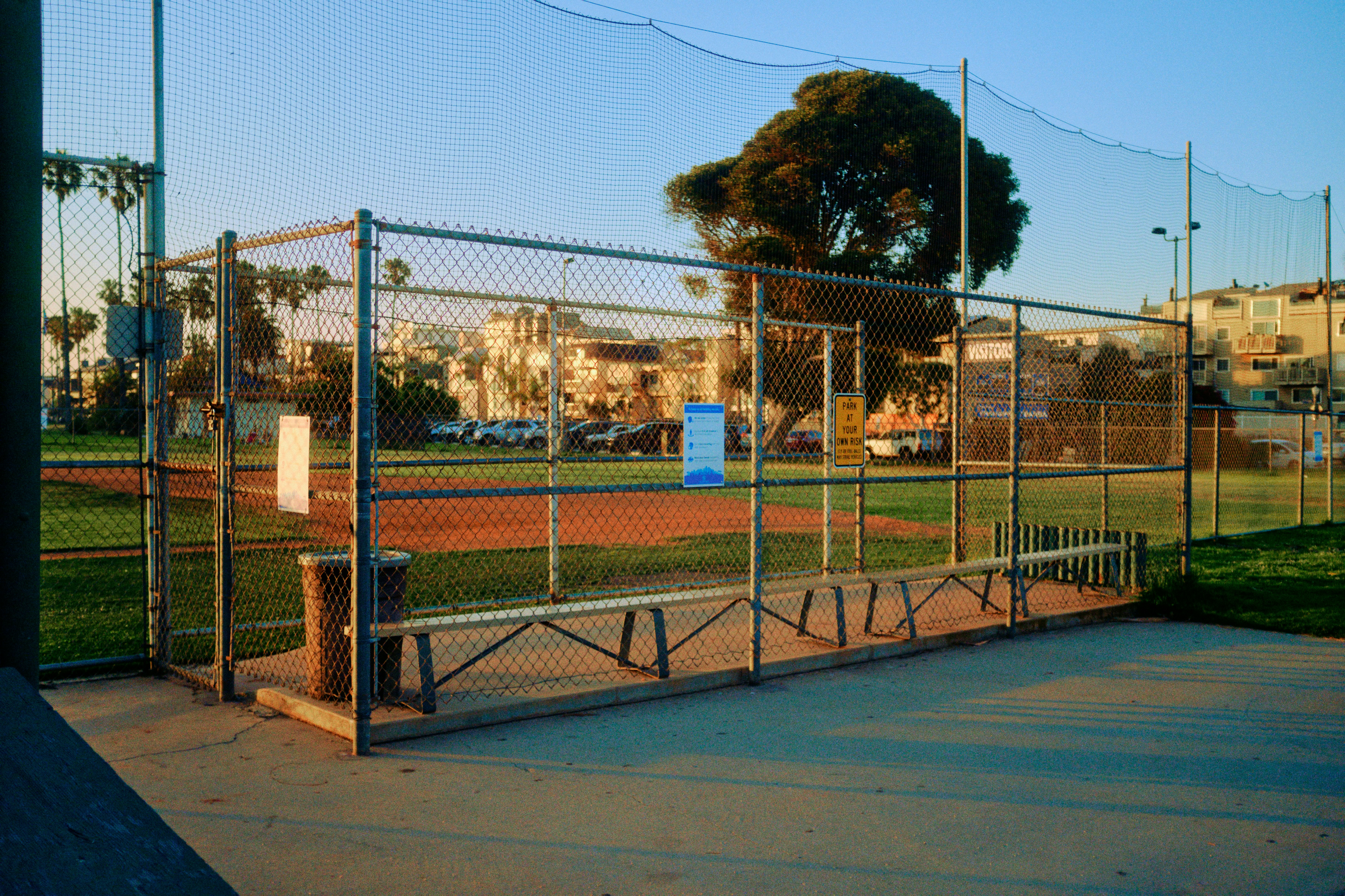 Empty baseball field with chain-link fencing and a bench under warm evening light.