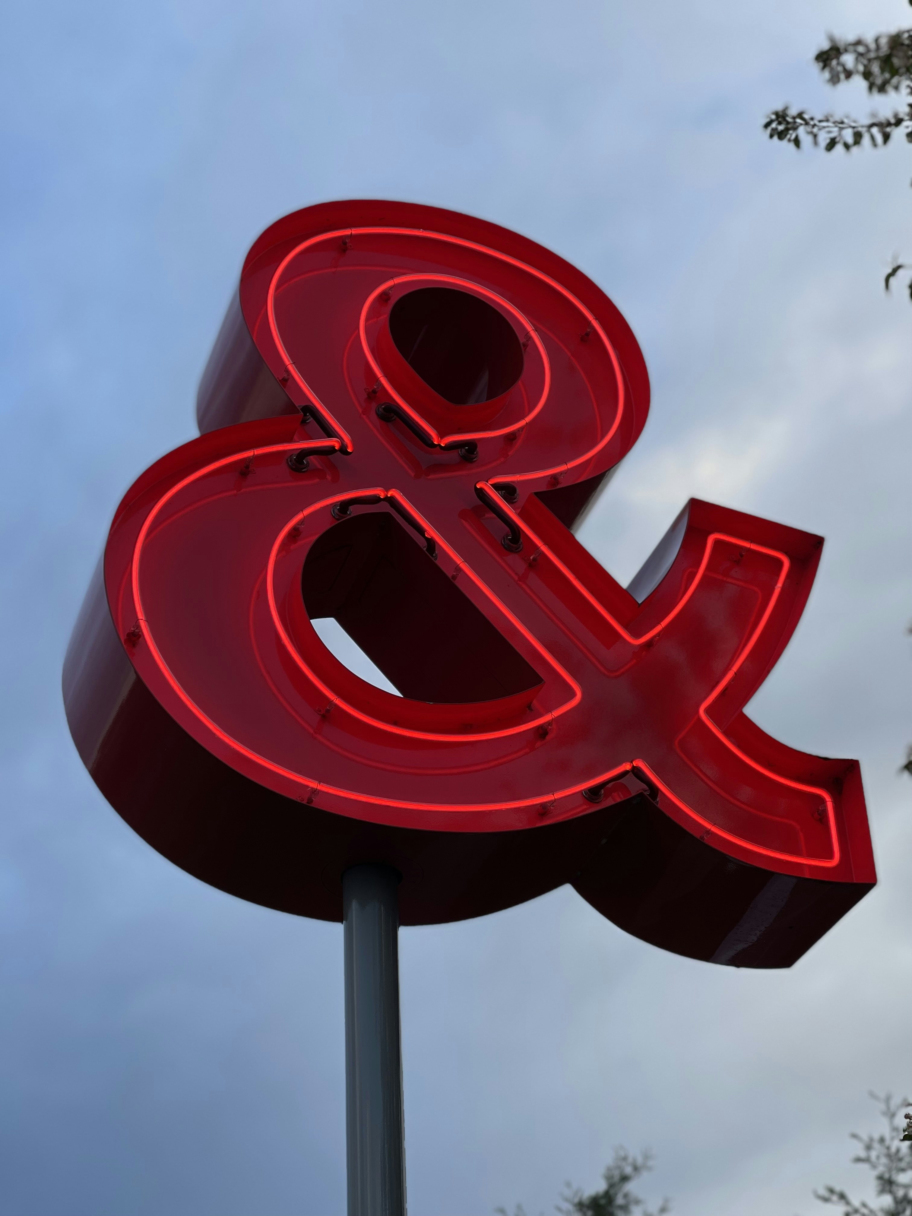 Bright red ampersand sign stands tall against a cloudy sky, symbolizing unity and partnership.