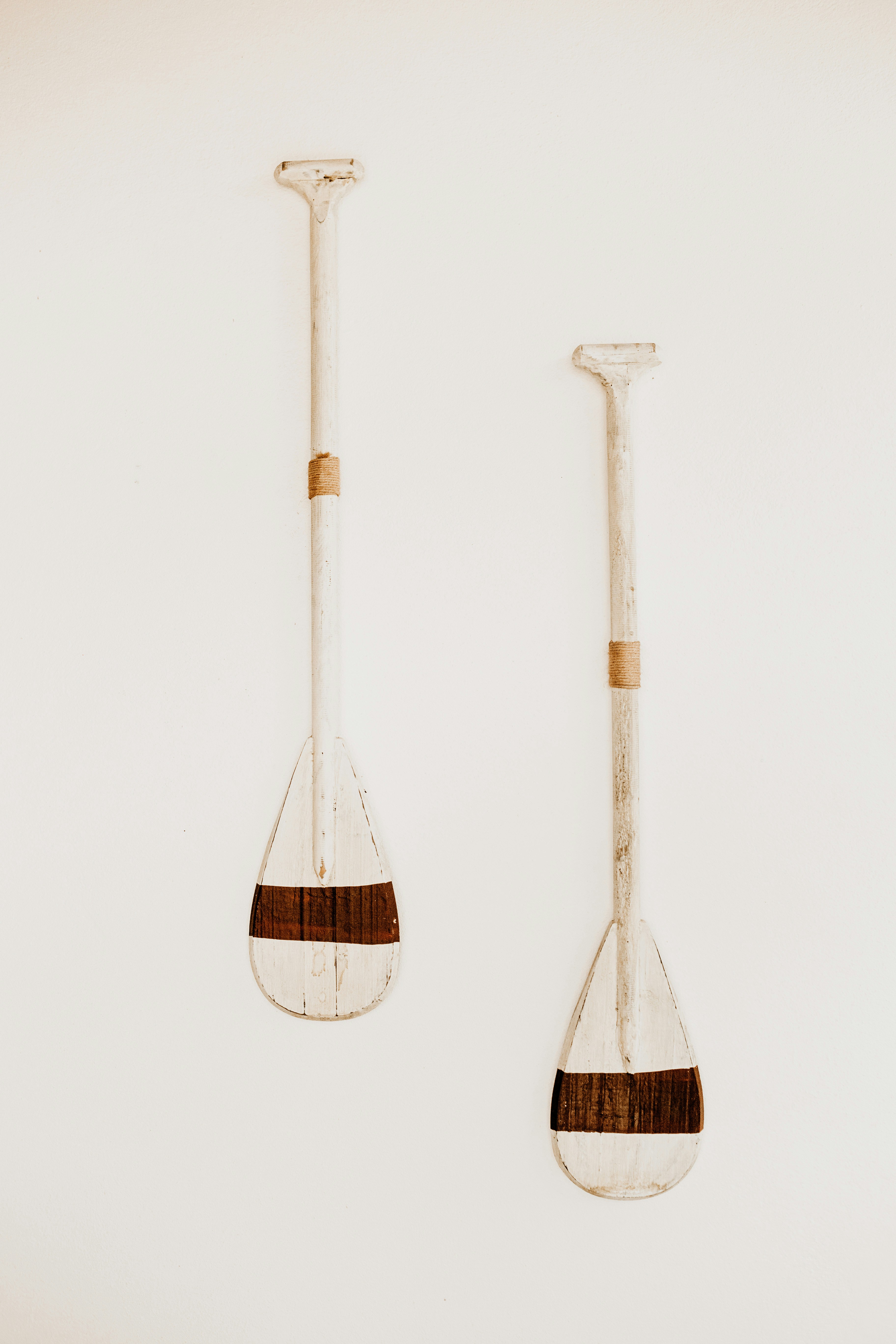 Two weathered oars suspended against a pale wall