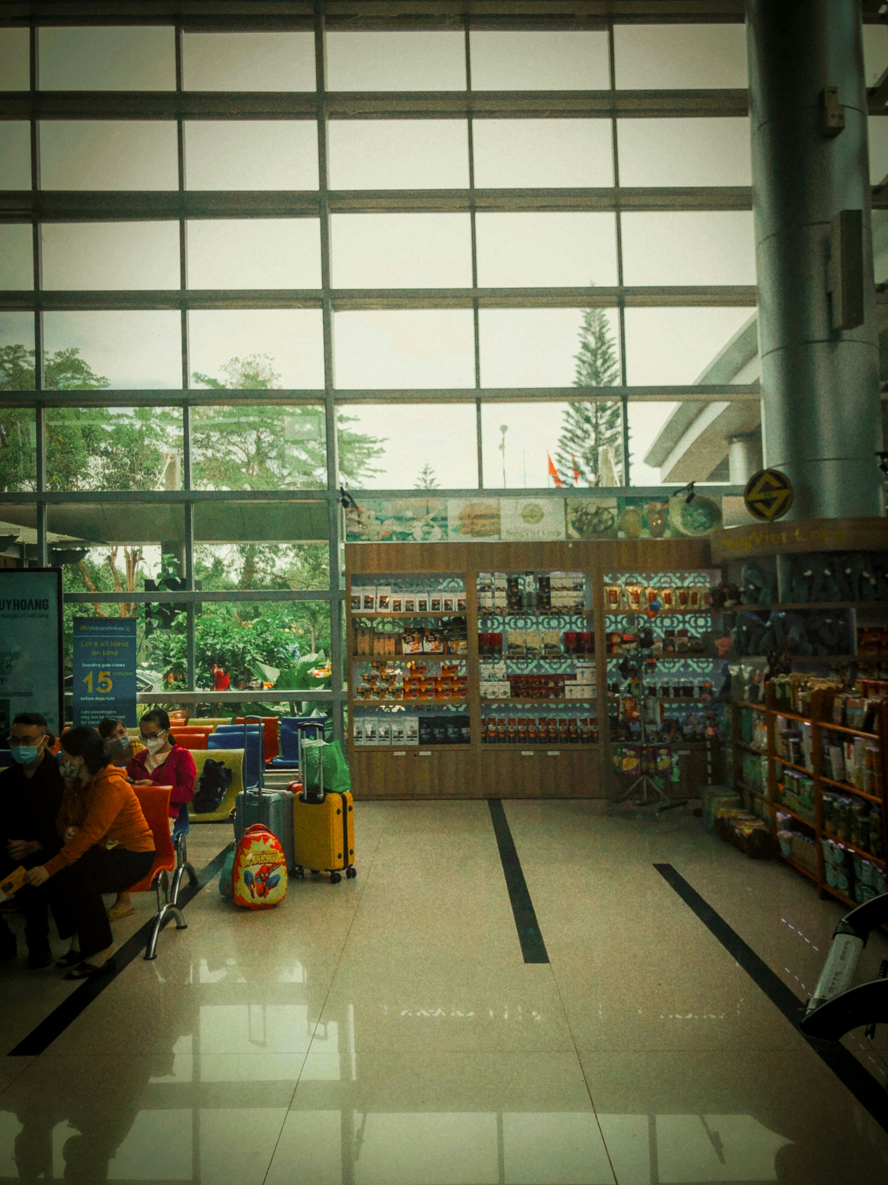 Sunlit Terminal Quiet: Masked Travelers in a Glass-Walled Shop
