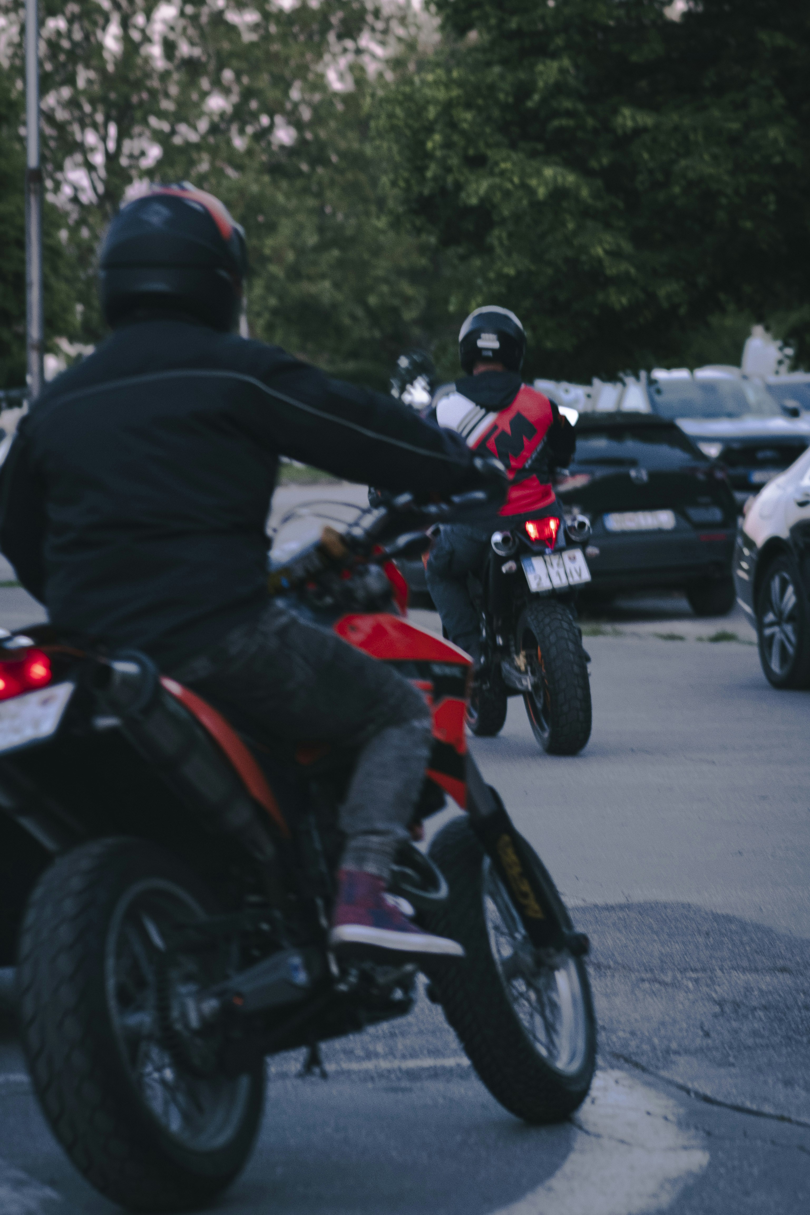 Two motorcyclists navigating through a cityscape, showcasing the blend of adventure and urban life. A glimpse of parked cars adds context to their journey.