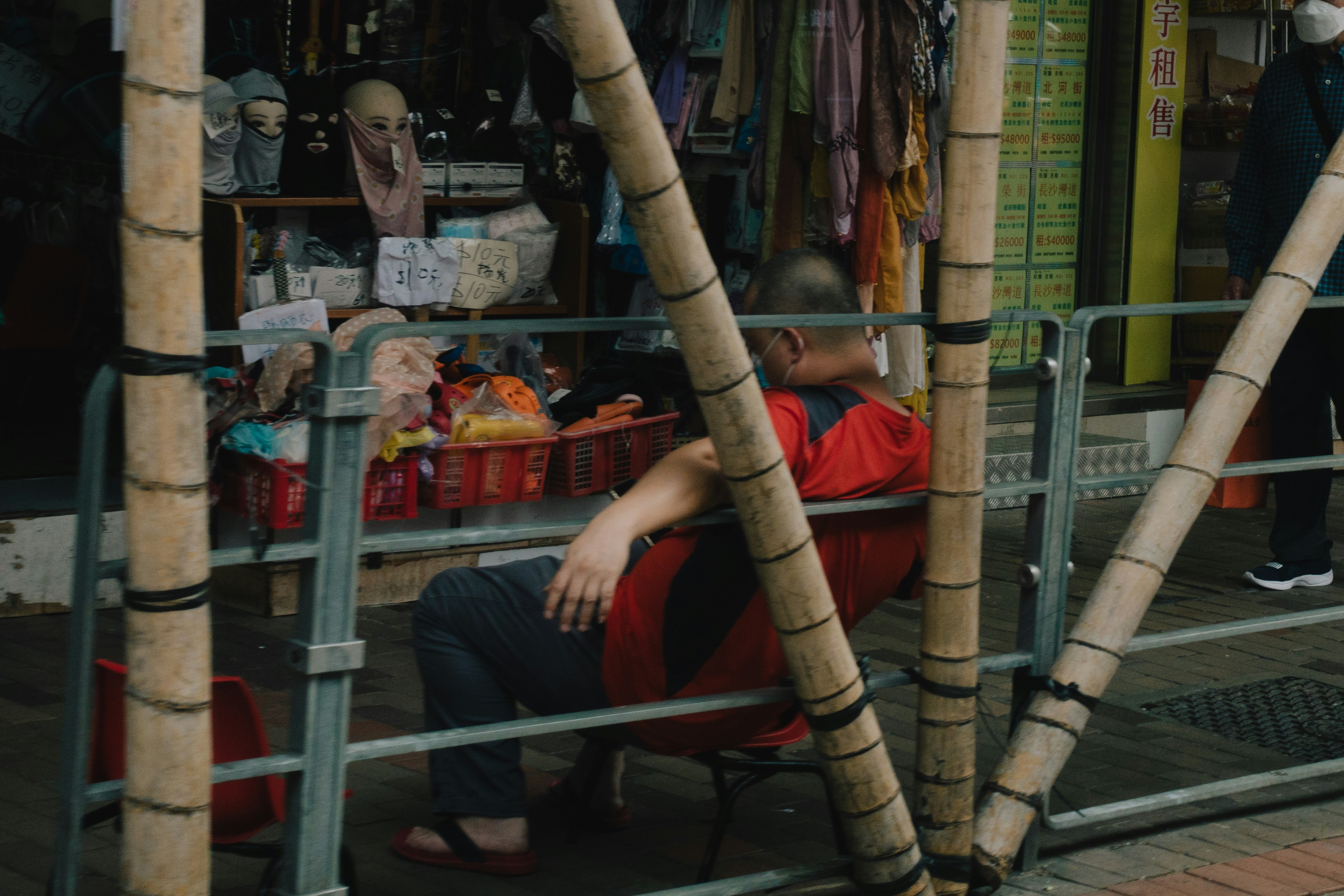 Red-Clad Pause Behind Bamboo Bars in a Market Corridor