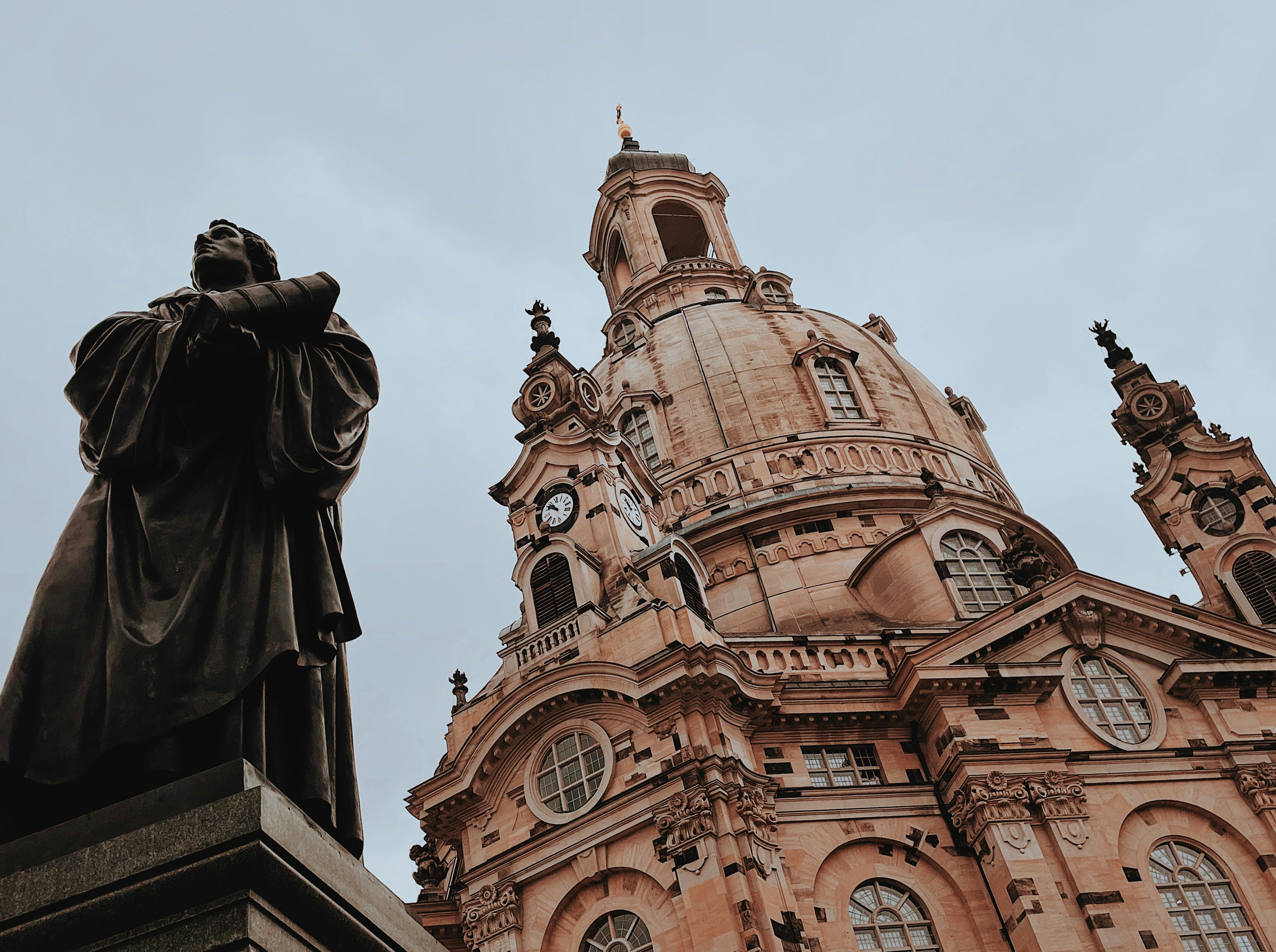 A statue stands in the foreground, gazing up at an intricately designed baroque church, showcasing a blend of artistry and architecture.