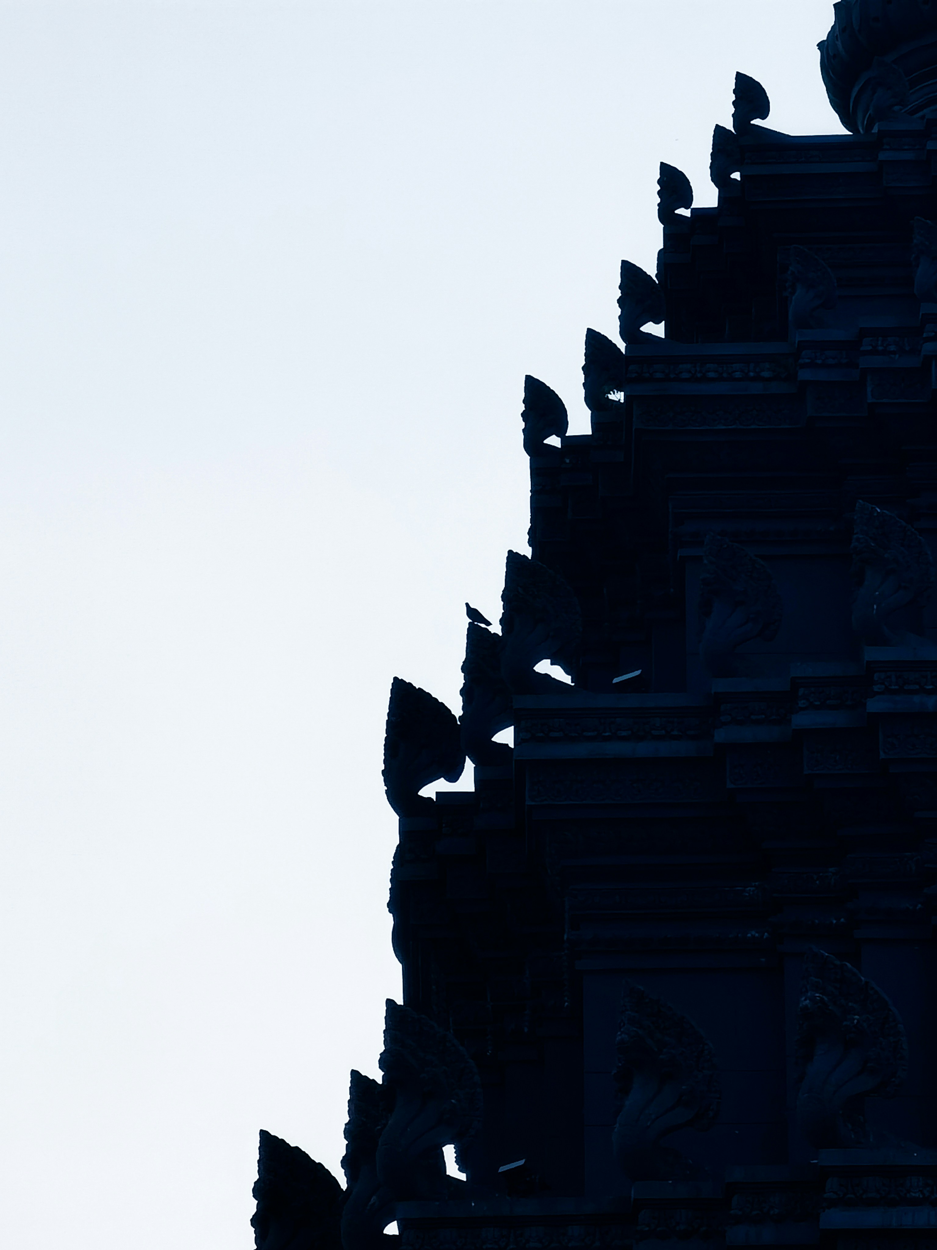 A silhouetted temple structure against a pale sky, showcasing intricate architectural details at the top. The image captures the essence of tranquility and reverence.