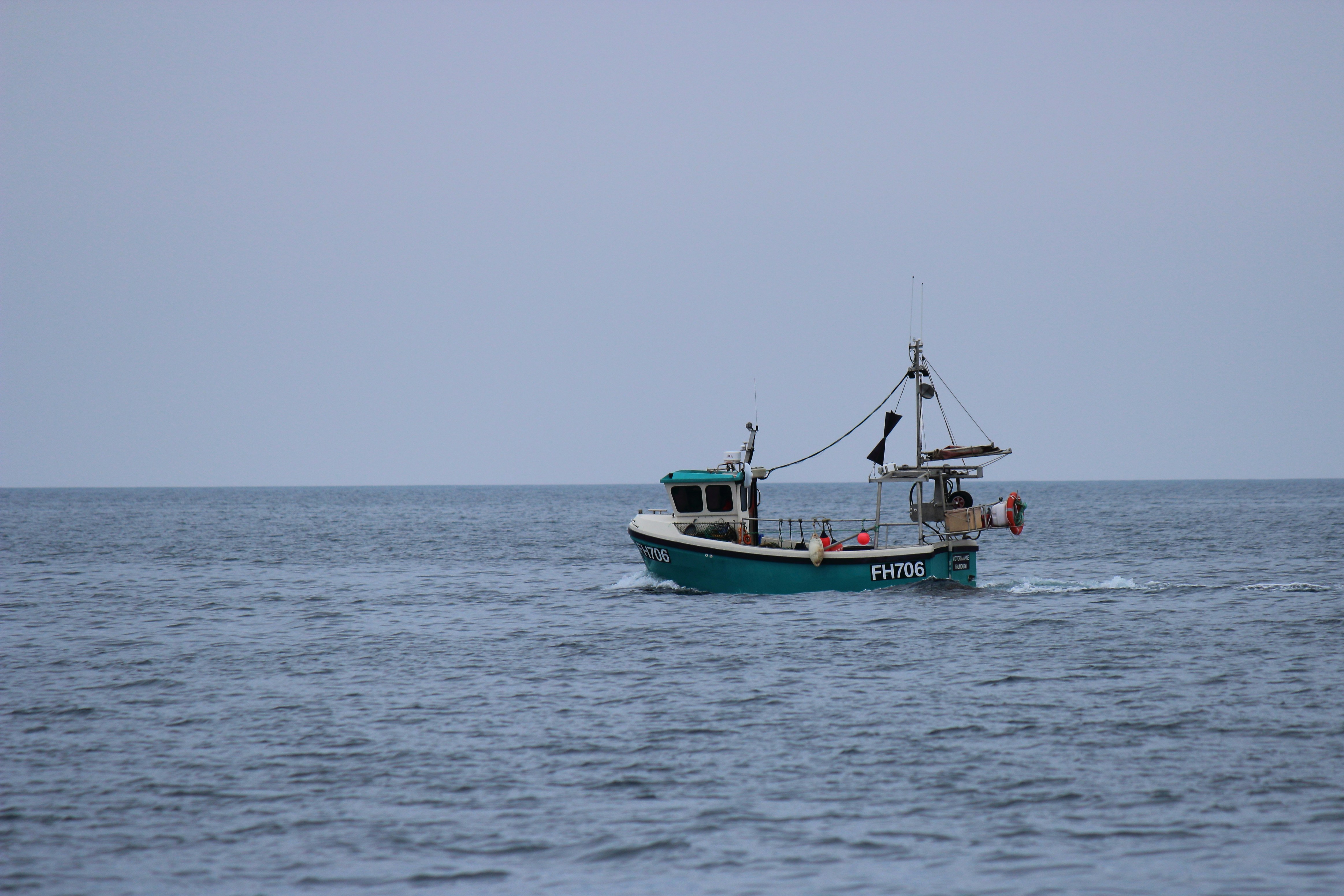Fishing boat navigating calm ocean waters under a muted sky.