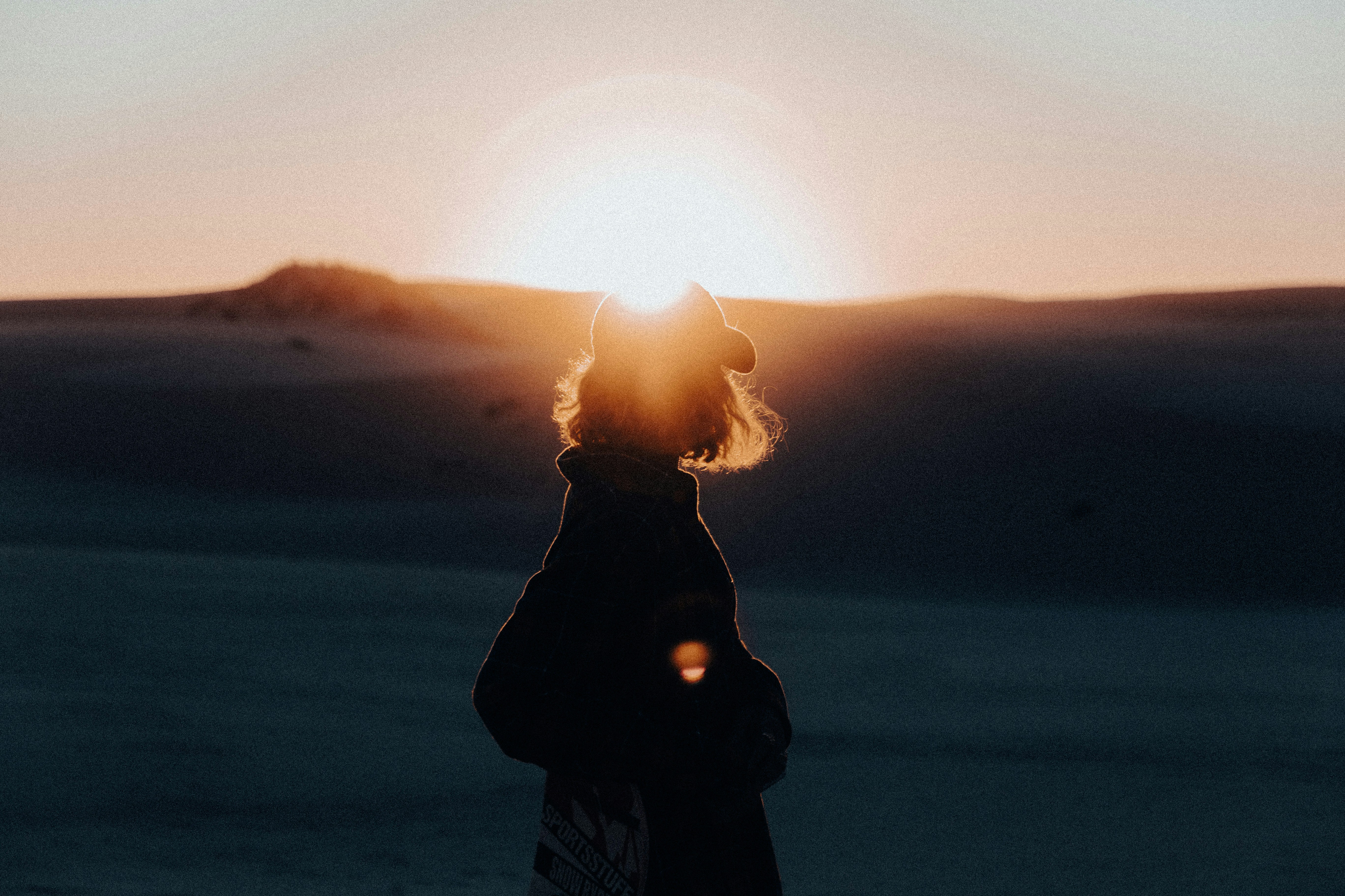 Silhouette of a person standing against a setting sun in a vast desert landscape, capturing a moment of reflection and solitude.
