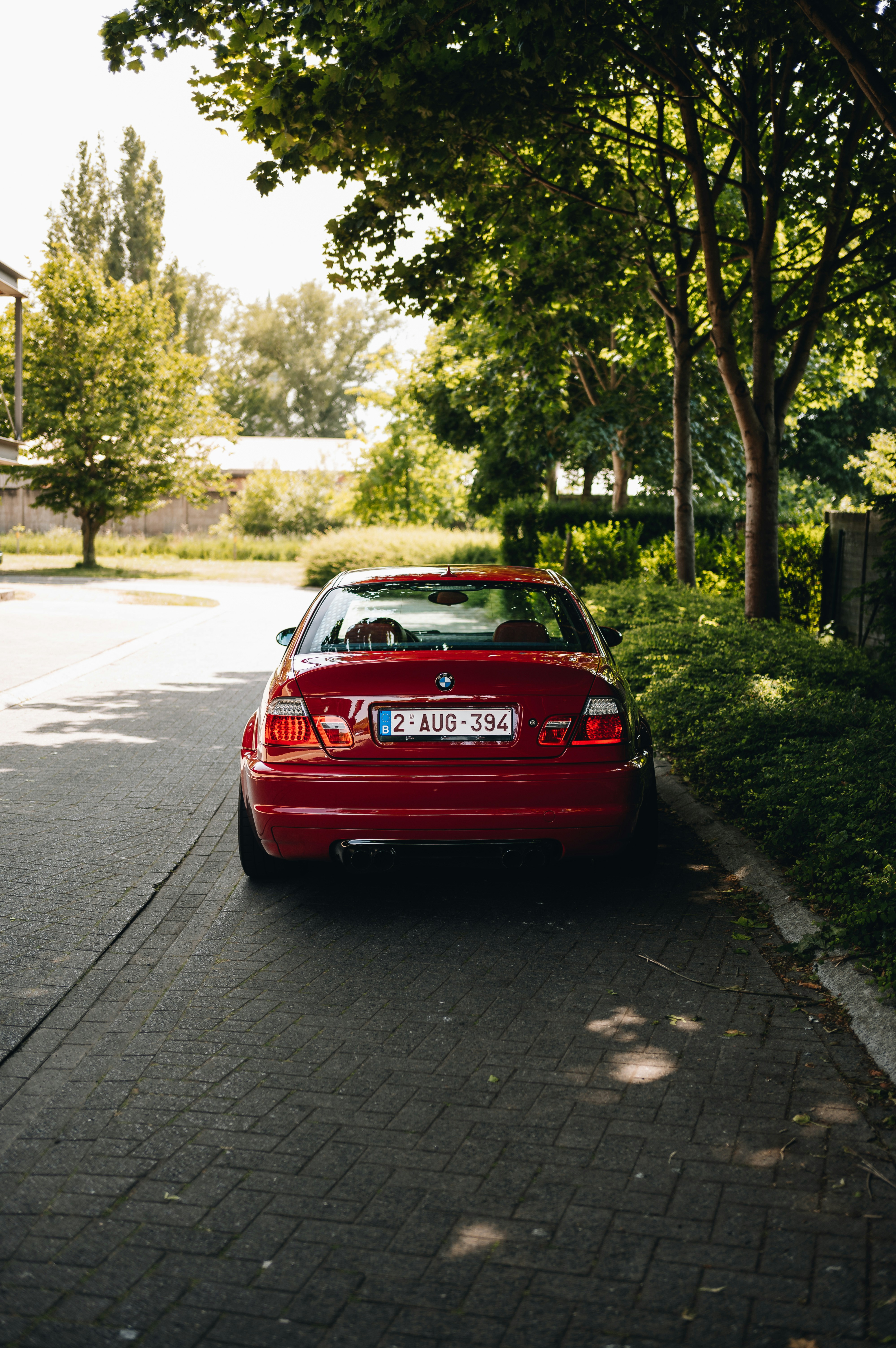 A vibrant red car parked along a tree-lined street, showcasing its sleek design against a backdrop of lush greenery.