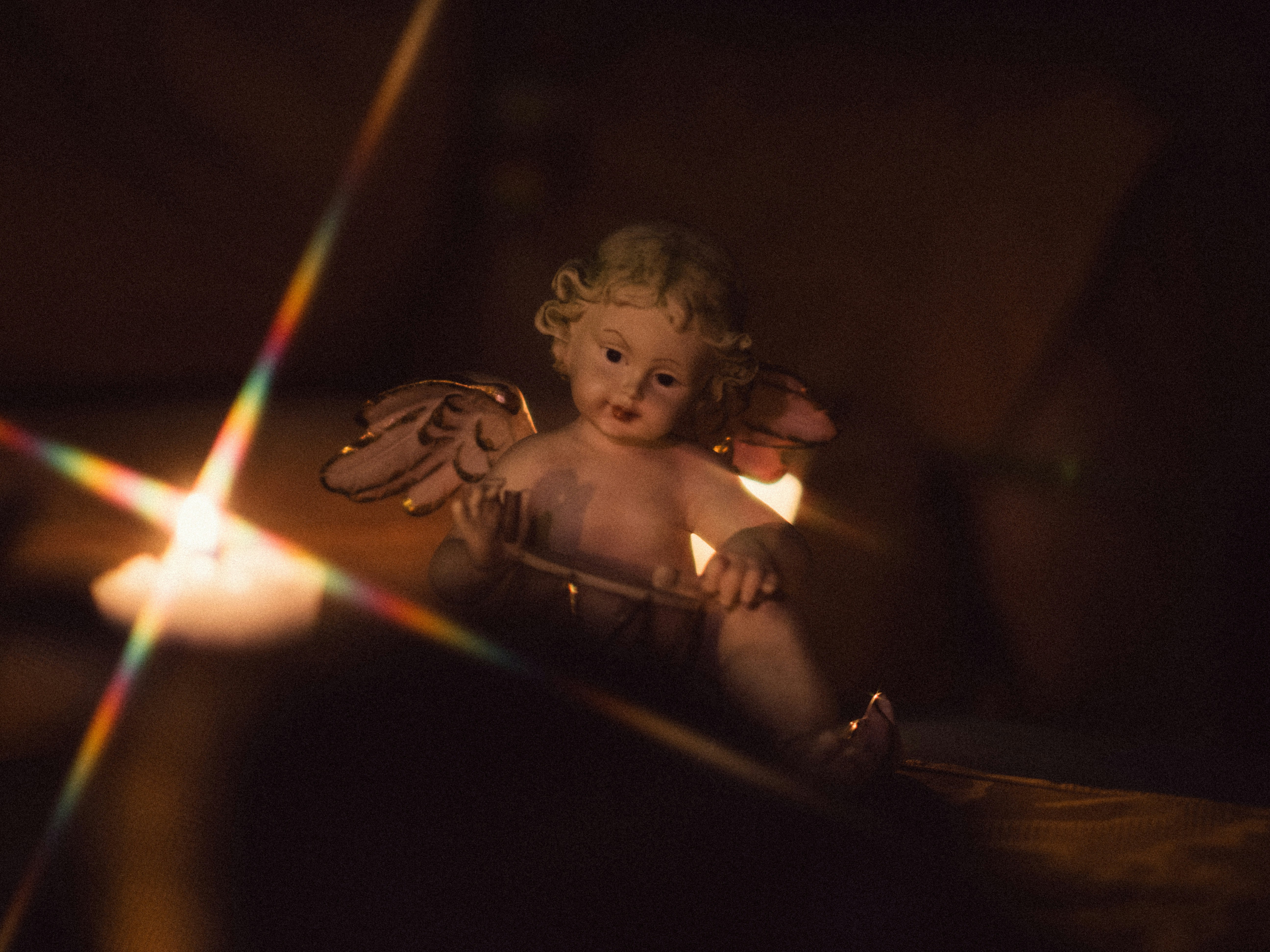 Cherub statue illuminated by candlelight with a soft, warm glow and lens flare effect.