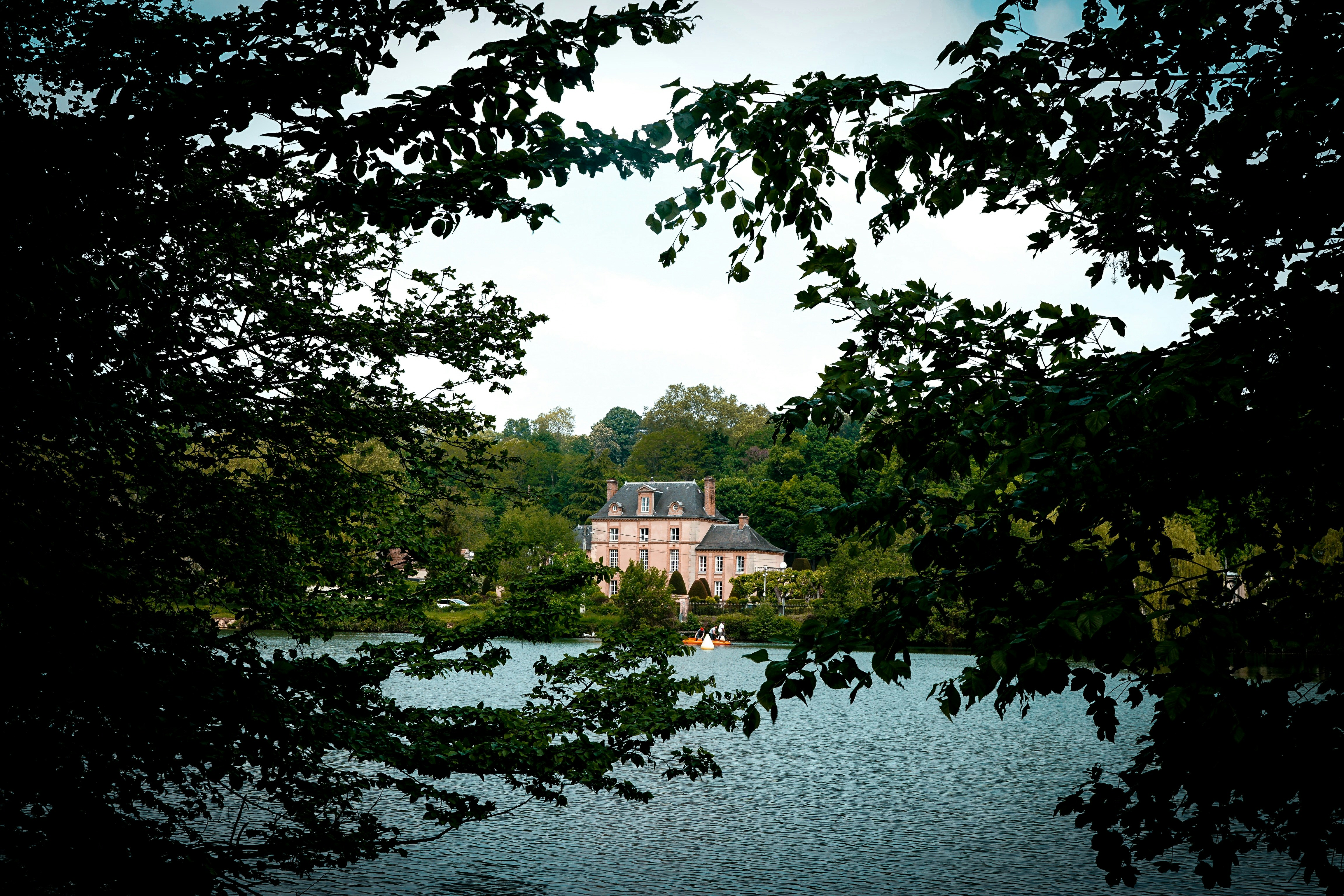 Historic mansion framed by lush foliage, overlooking a serene lake. A tranquil scene that invites reflection.