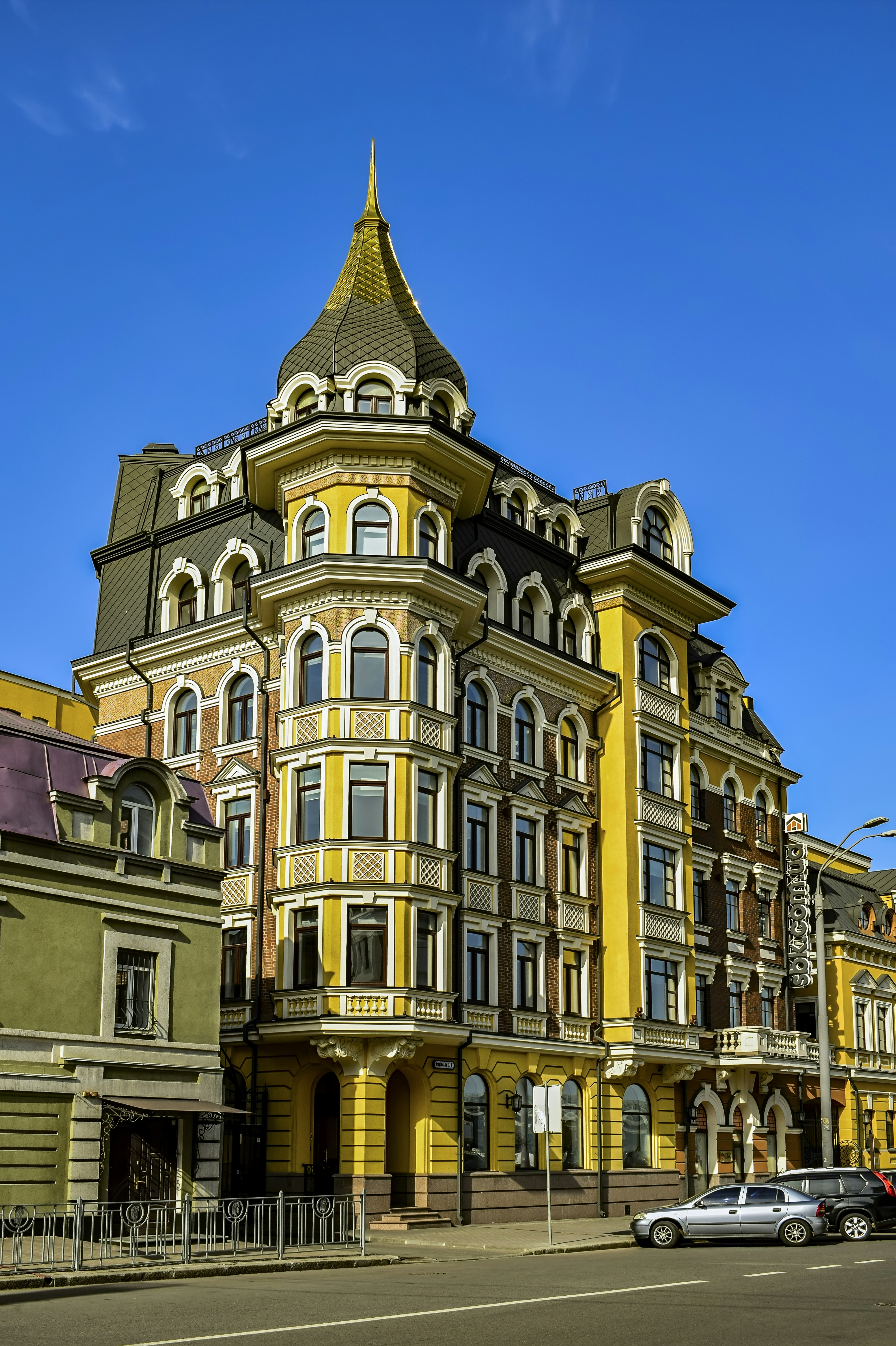 Intricate yellow and gray building with a distinctive golden spire, showcasing ornate architectural details against a clear blue sky.