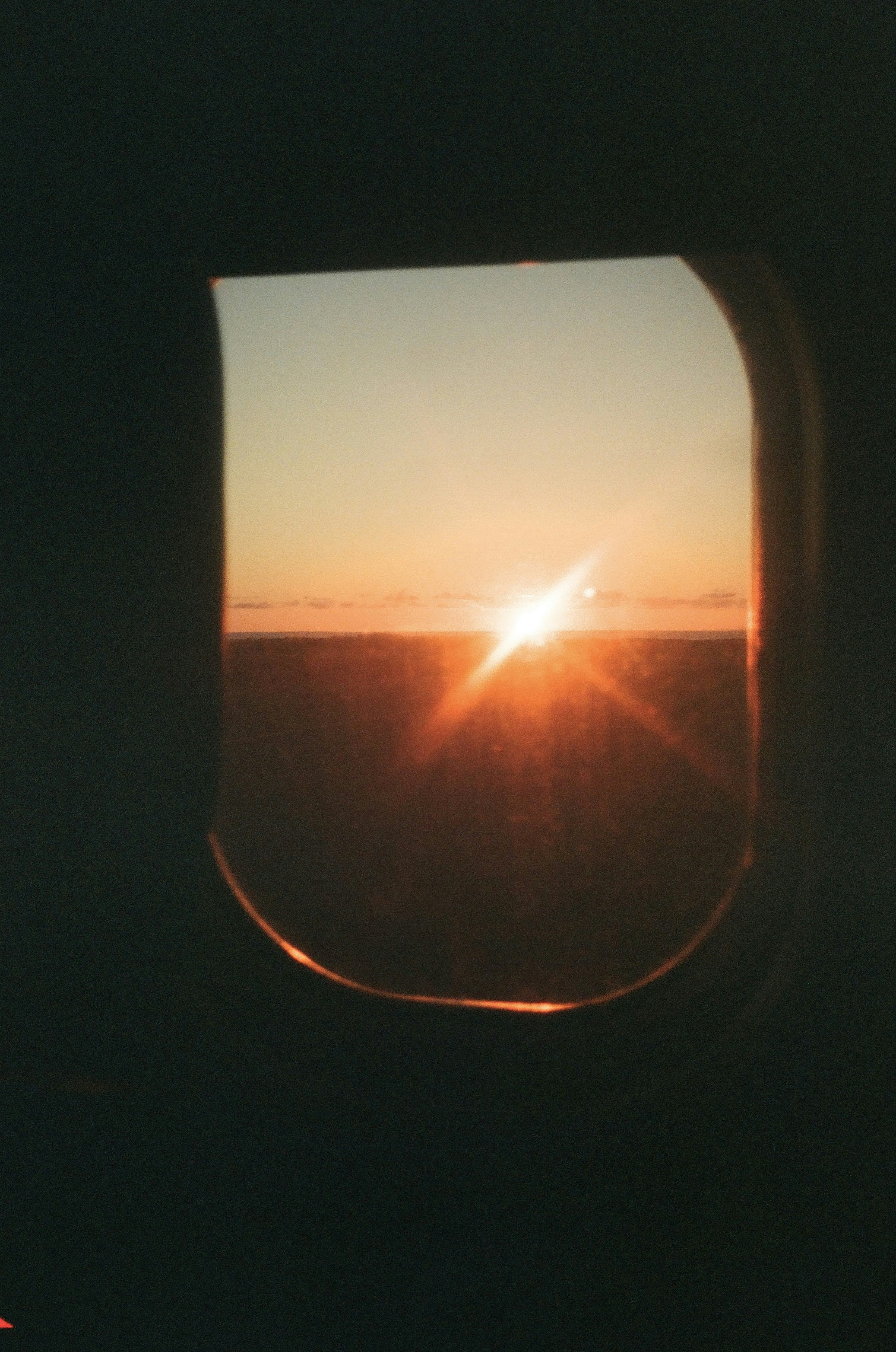 Golden sunset viewed through an airplane window, casting reflections on the glass. A serene moment captured in flight.