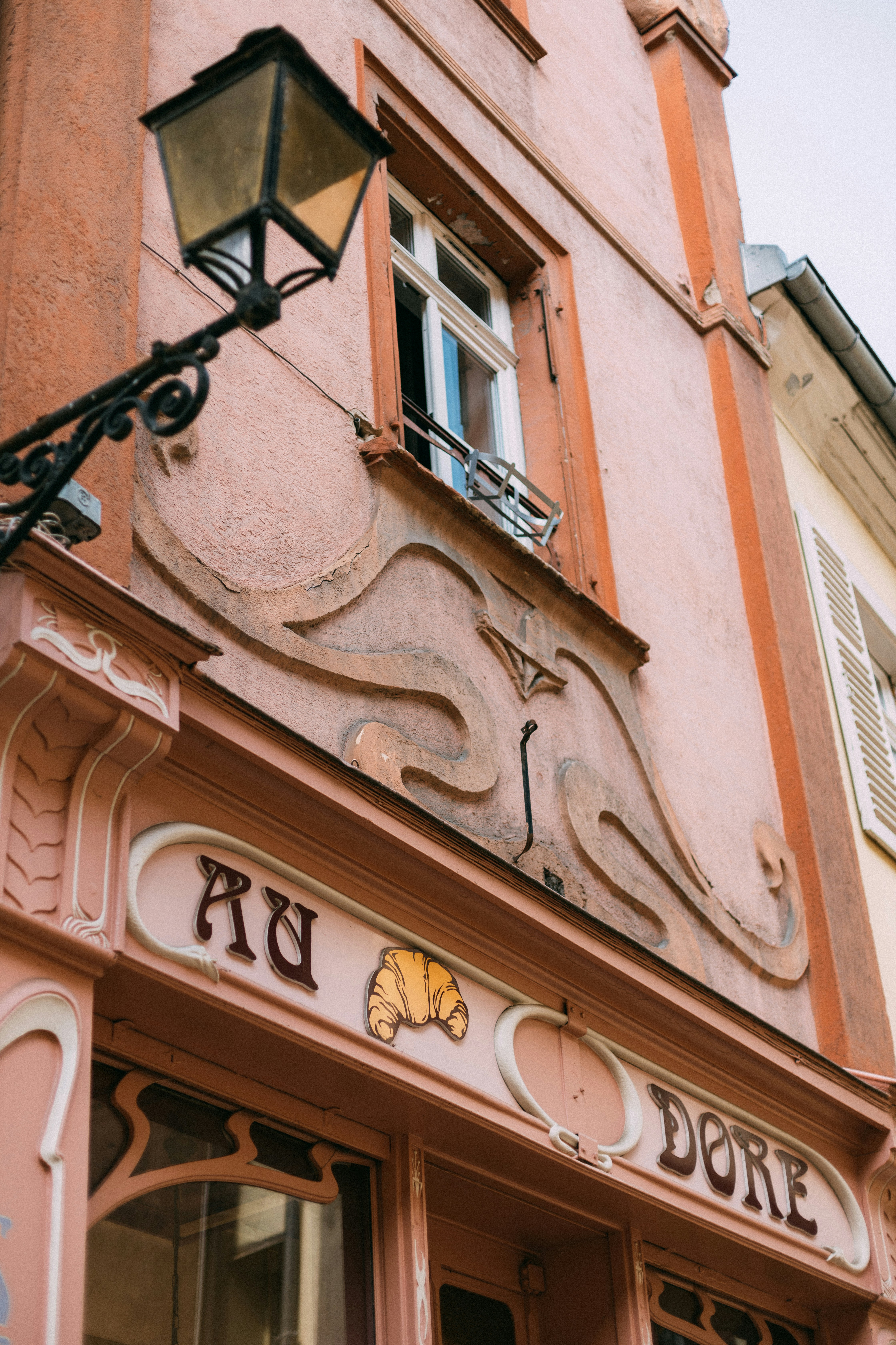 Pastel Shopfront: Ornate Relief, Shell Motif, and a Vintage Lantern