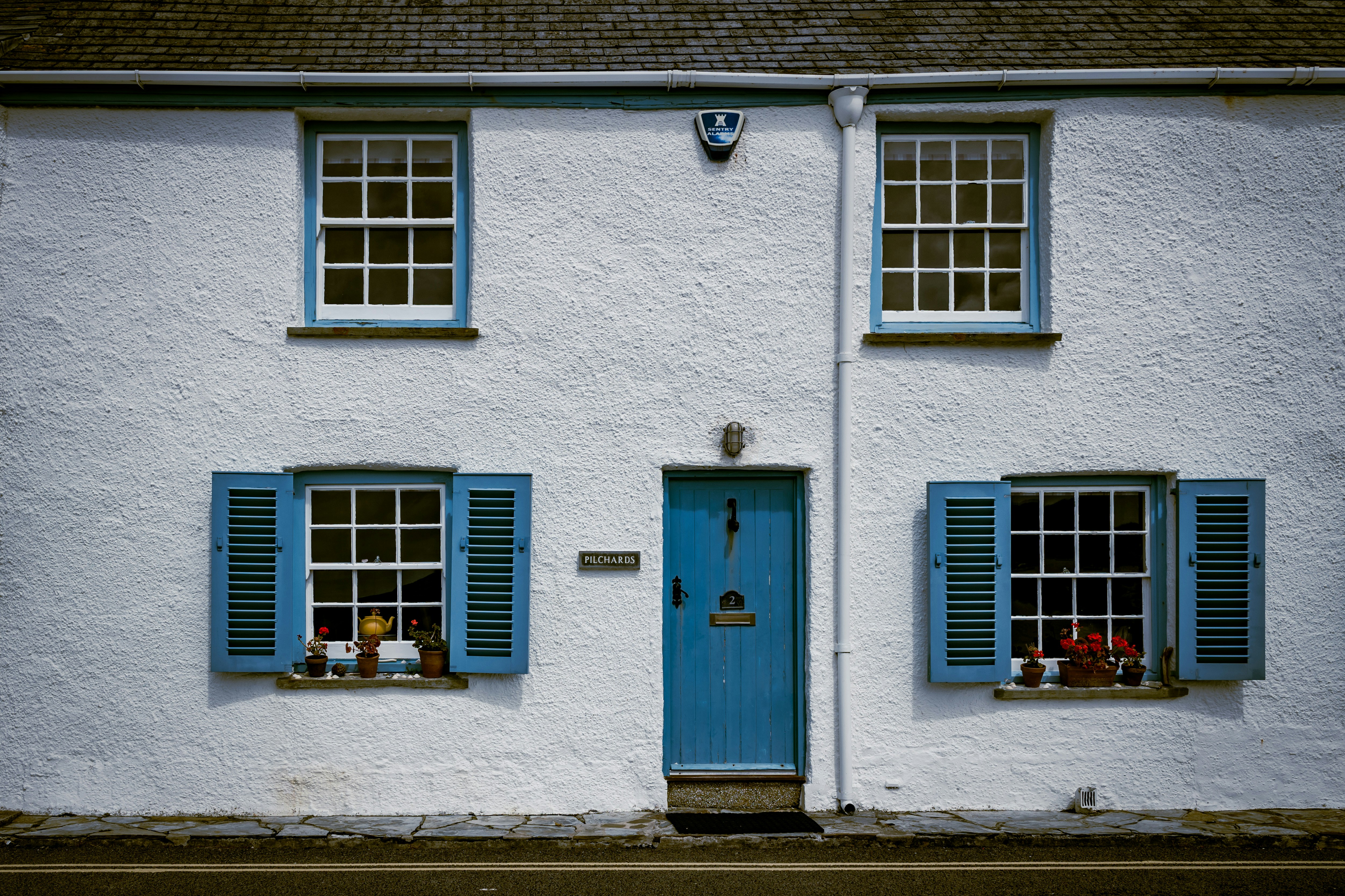 White house with blue shutters and door, adorned with colorful window displays.
