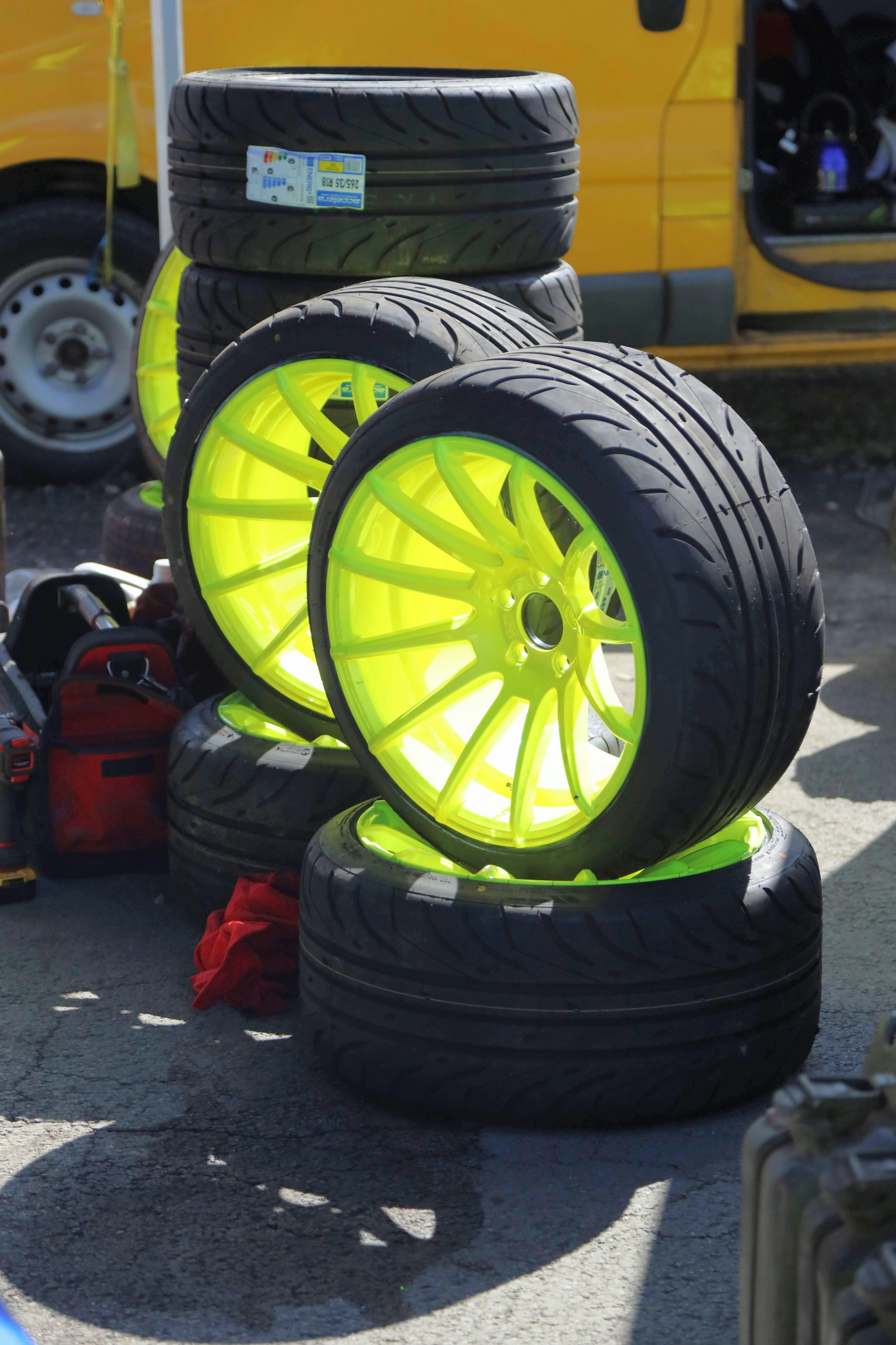 Neon-Lime Wheels Emerge from a Tire Stack beside a Bright Yellow Van