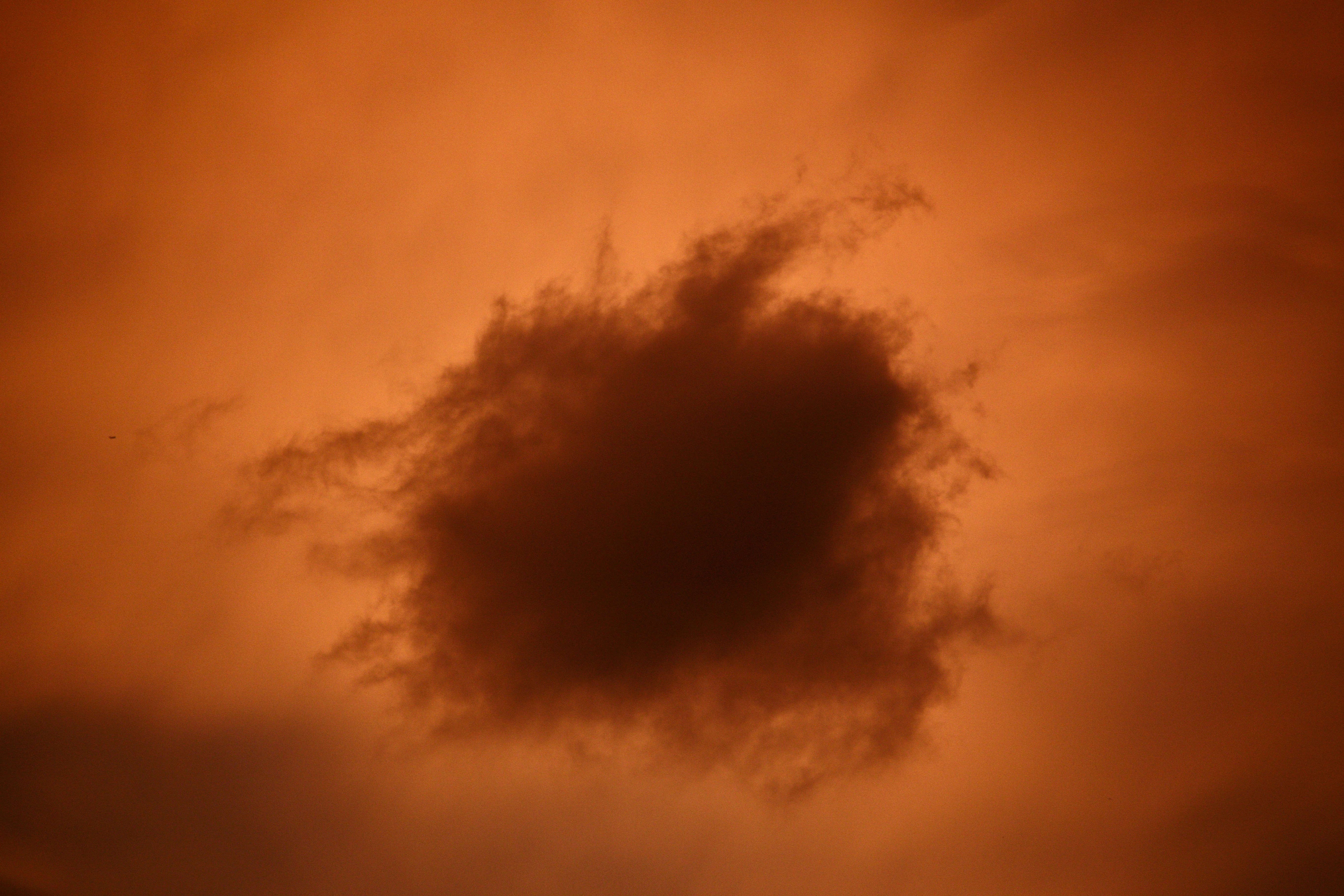 A solitary dark cloud floats against a backdrop of vibrant orange sky, evoking a sense of tranquility and introspection.