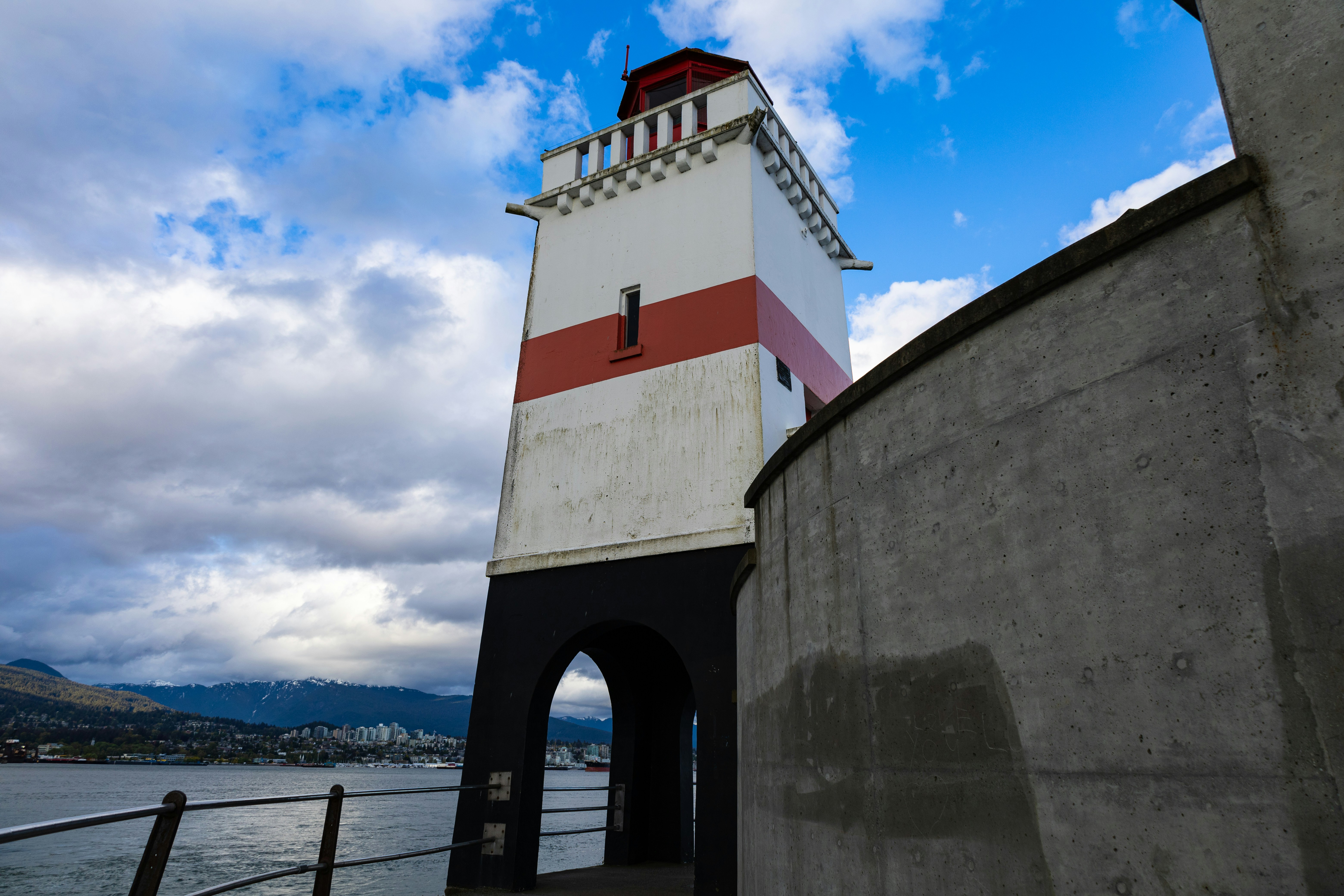 Tall lighthouse with a red band stands against a backdrop of clouds and distant mountains.