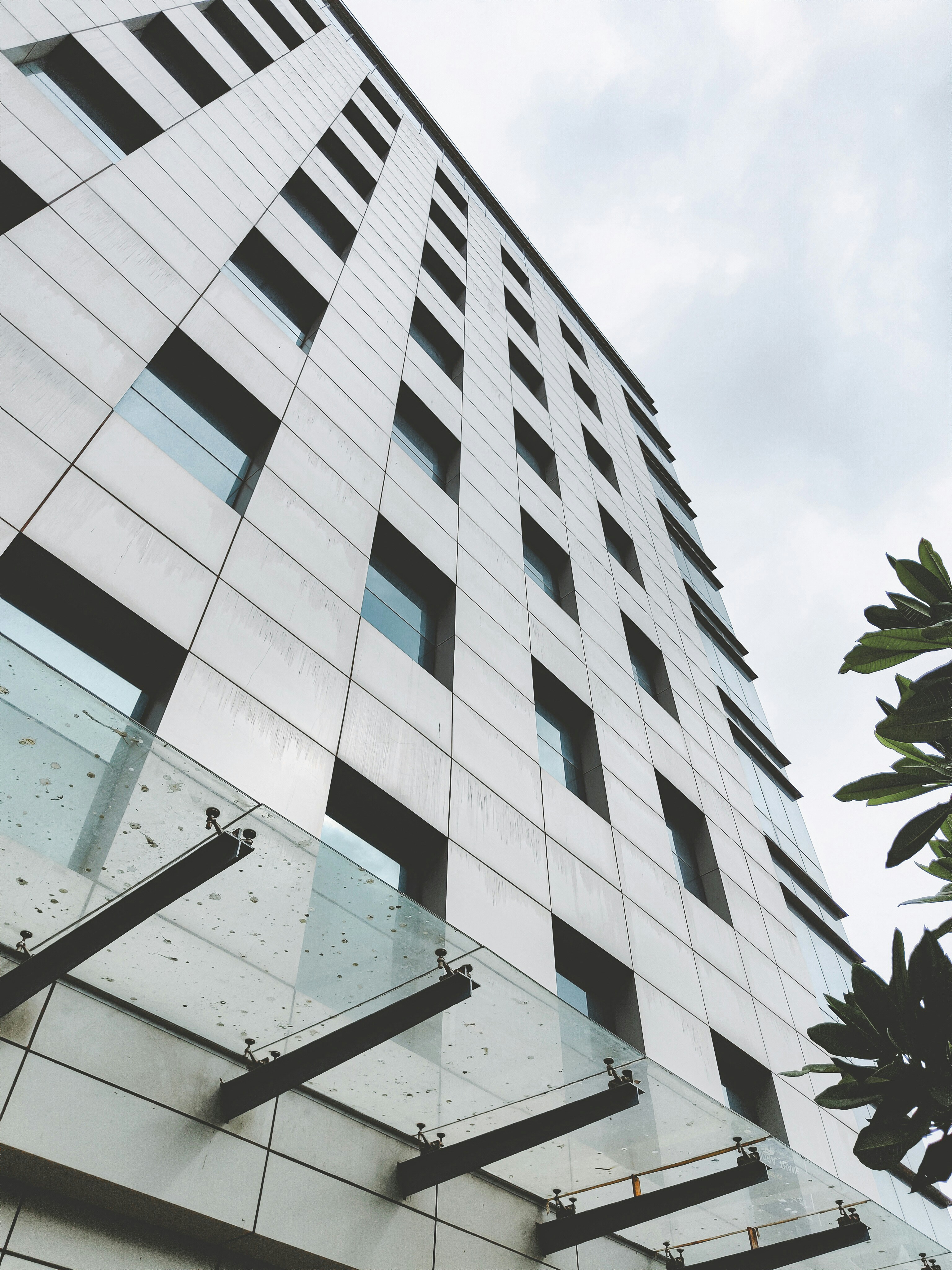 A contemporary building facade captured from a low angle, highlighting its geometric patterns and glass elements. The overcast sky adds a dramatic backdrop.