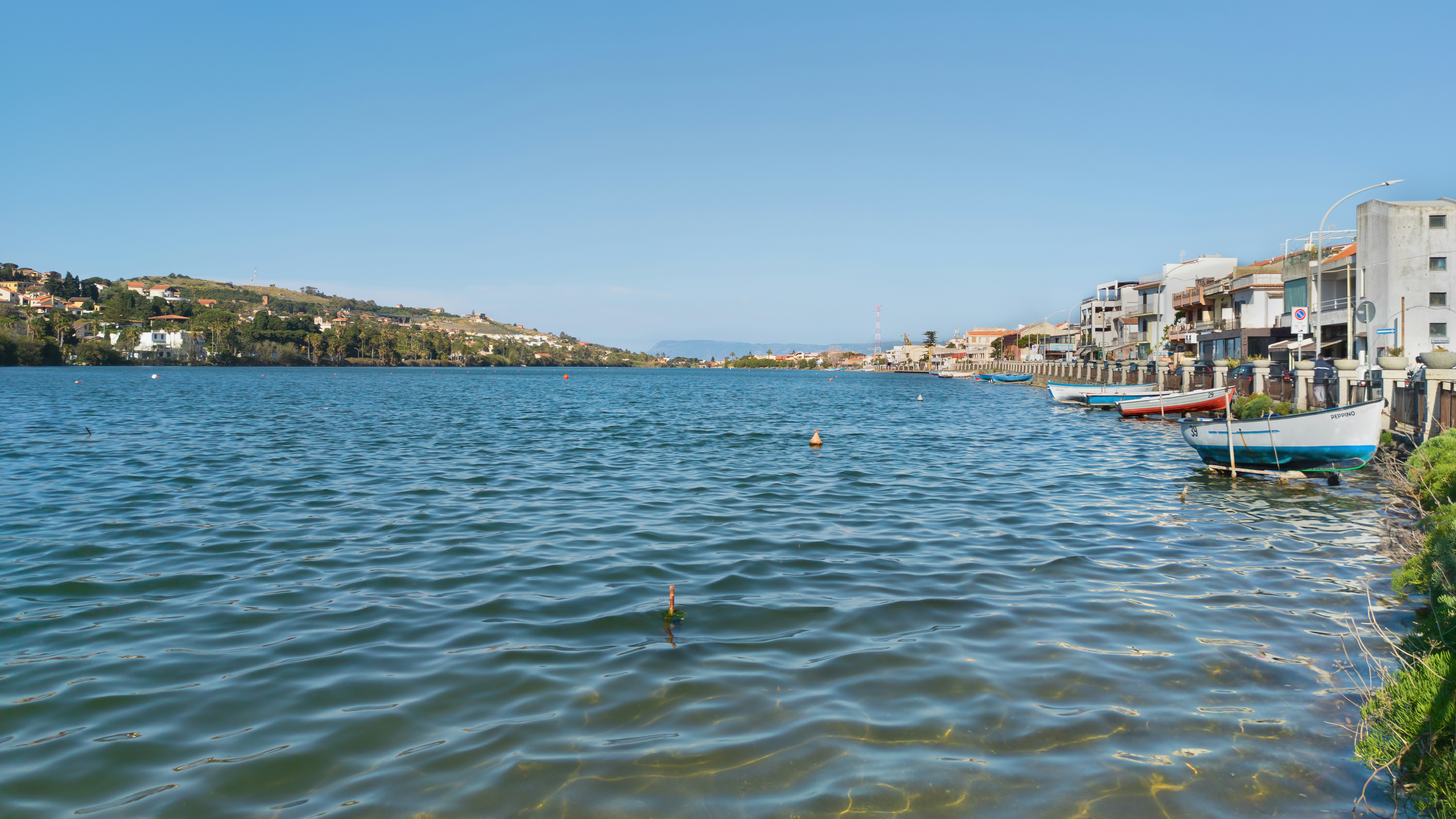 Calm blue waters reflecting a clear sky with boats moored along a residential shoreline.