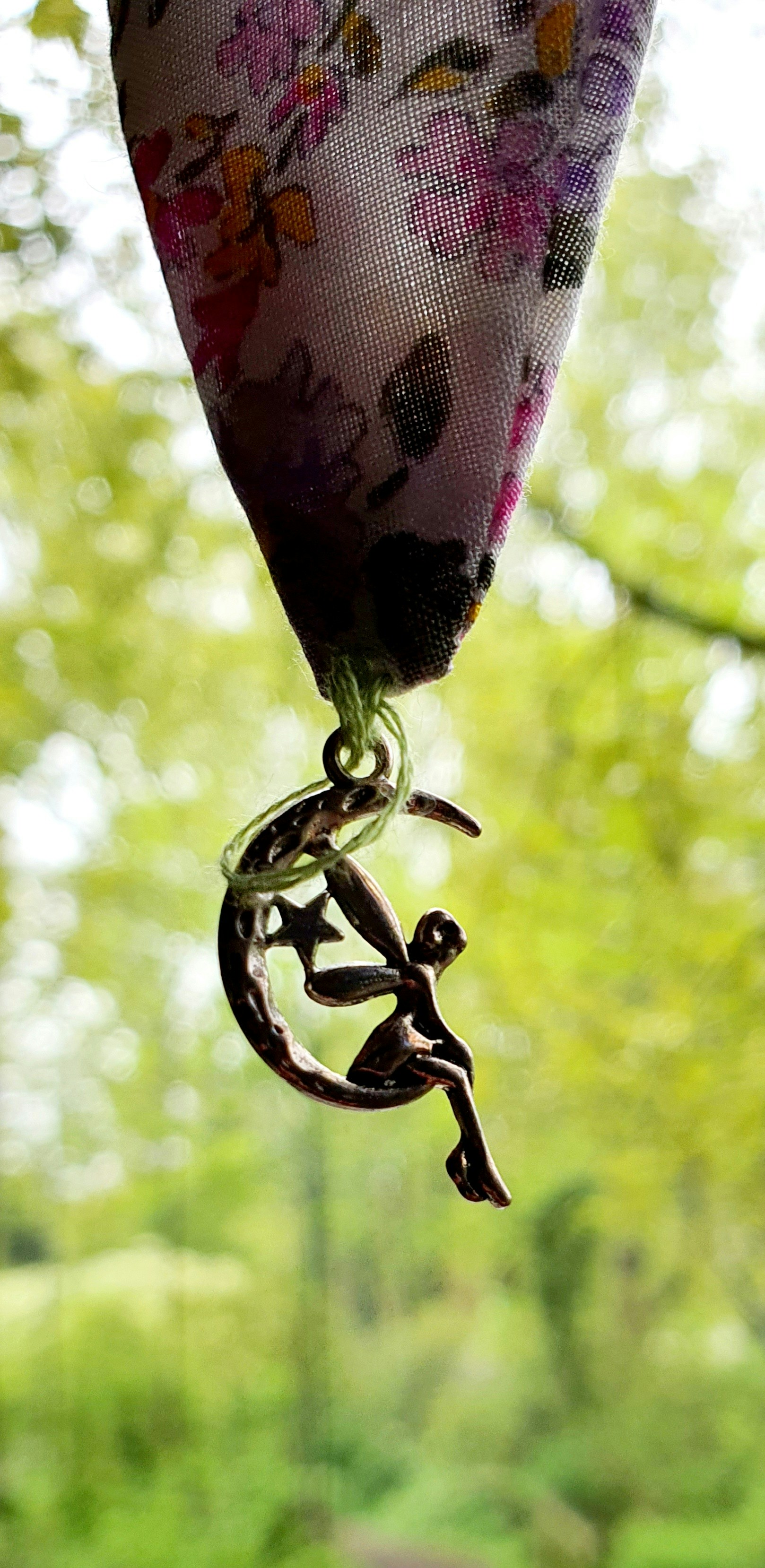 Forest Sunlight Reveals a Bronze Acrobat Pendant on a Floral Ribbon