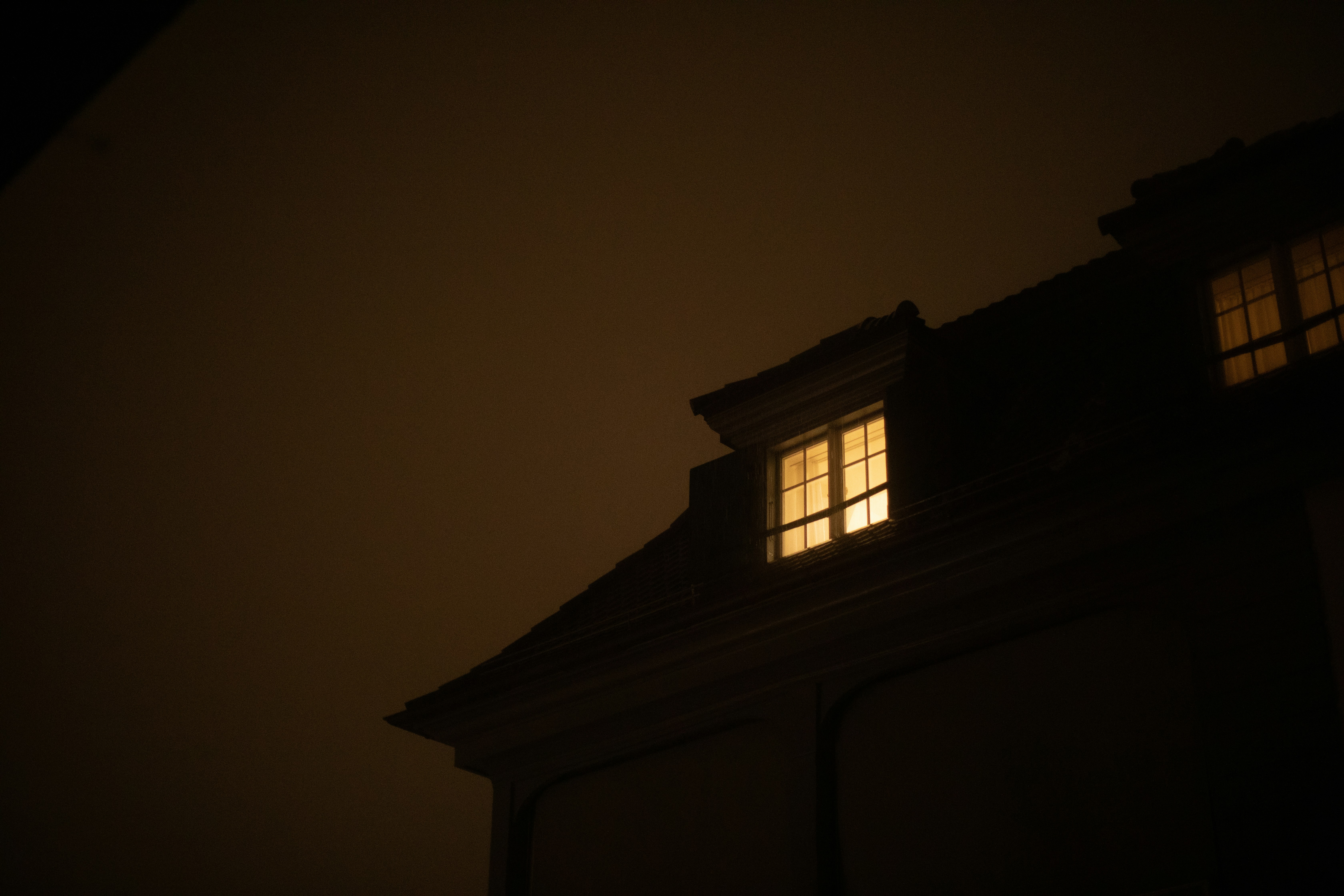Illuminated window on a dimly lit building against a hazy backdrop, suggesting a sense of mystery and solitude.