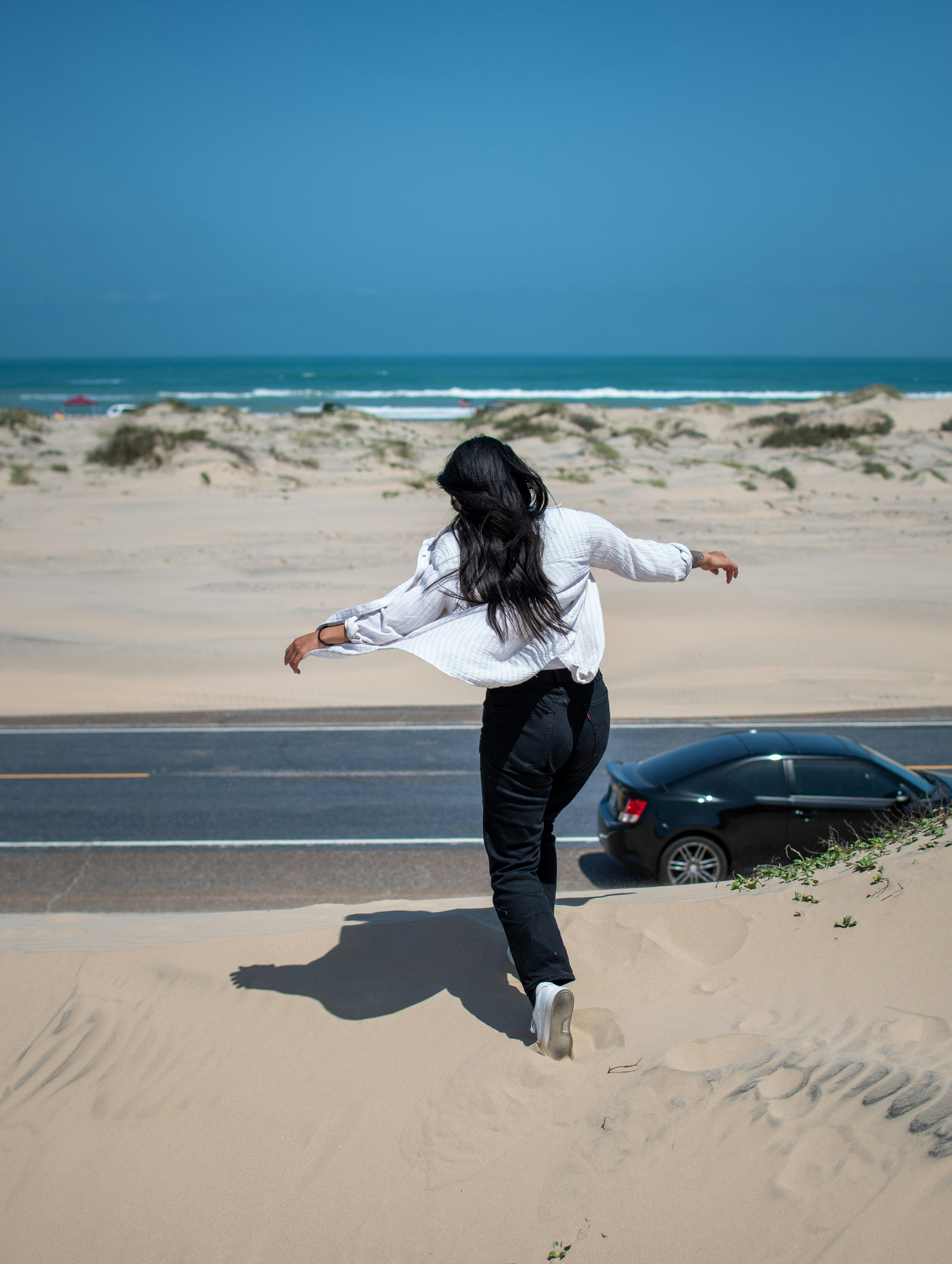 a woman standing in the sand near a car