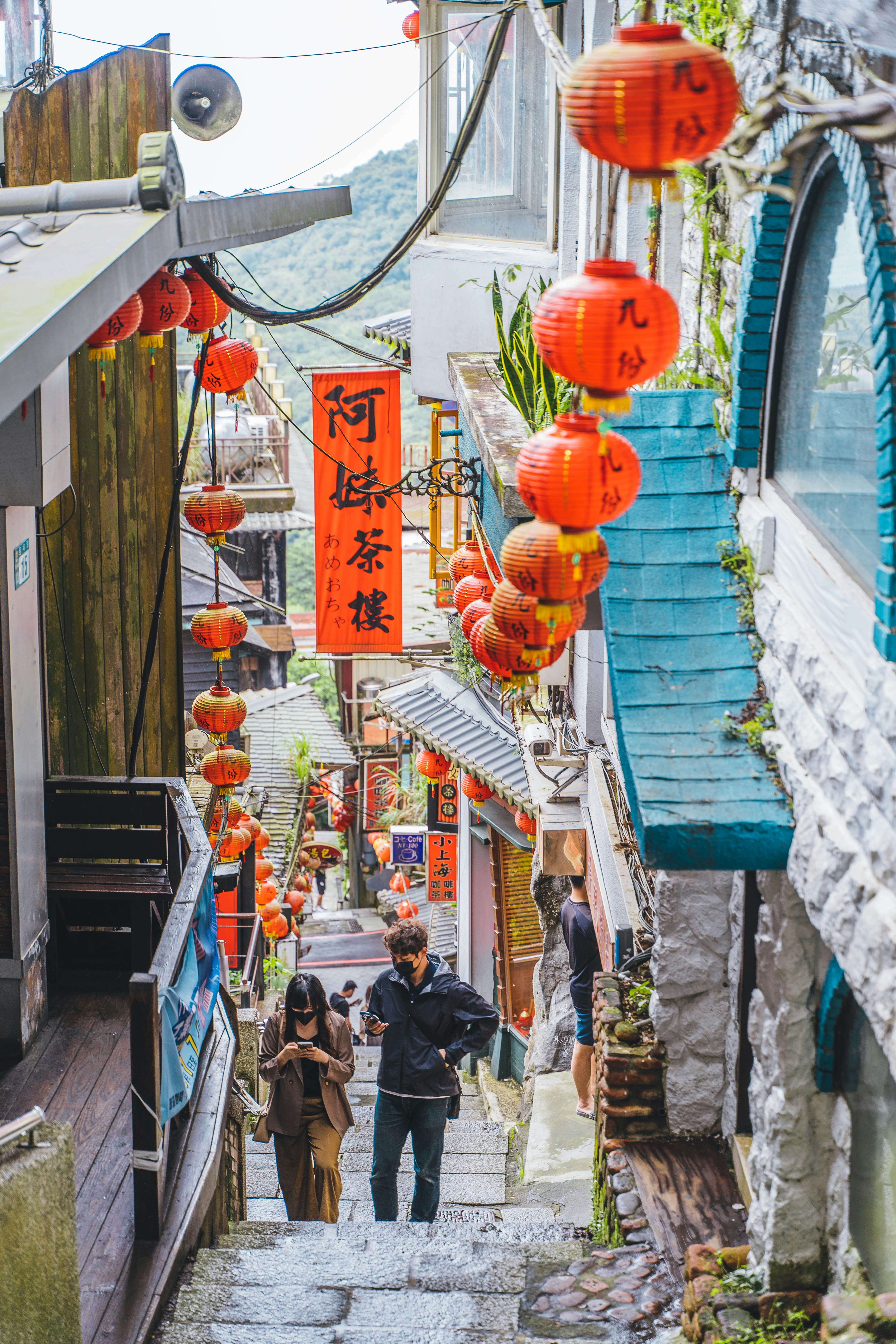 Visitors stroll down a narrow, lantern-adorned alley in a historic district, surrounded by vibrant signage and charming architecture.